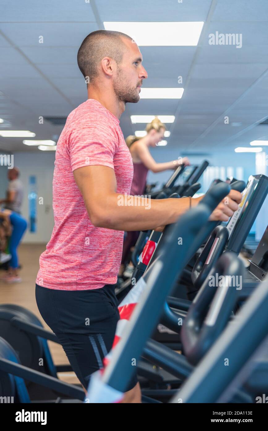 Side view of handsome male doing exercises on elliptical machine during ...