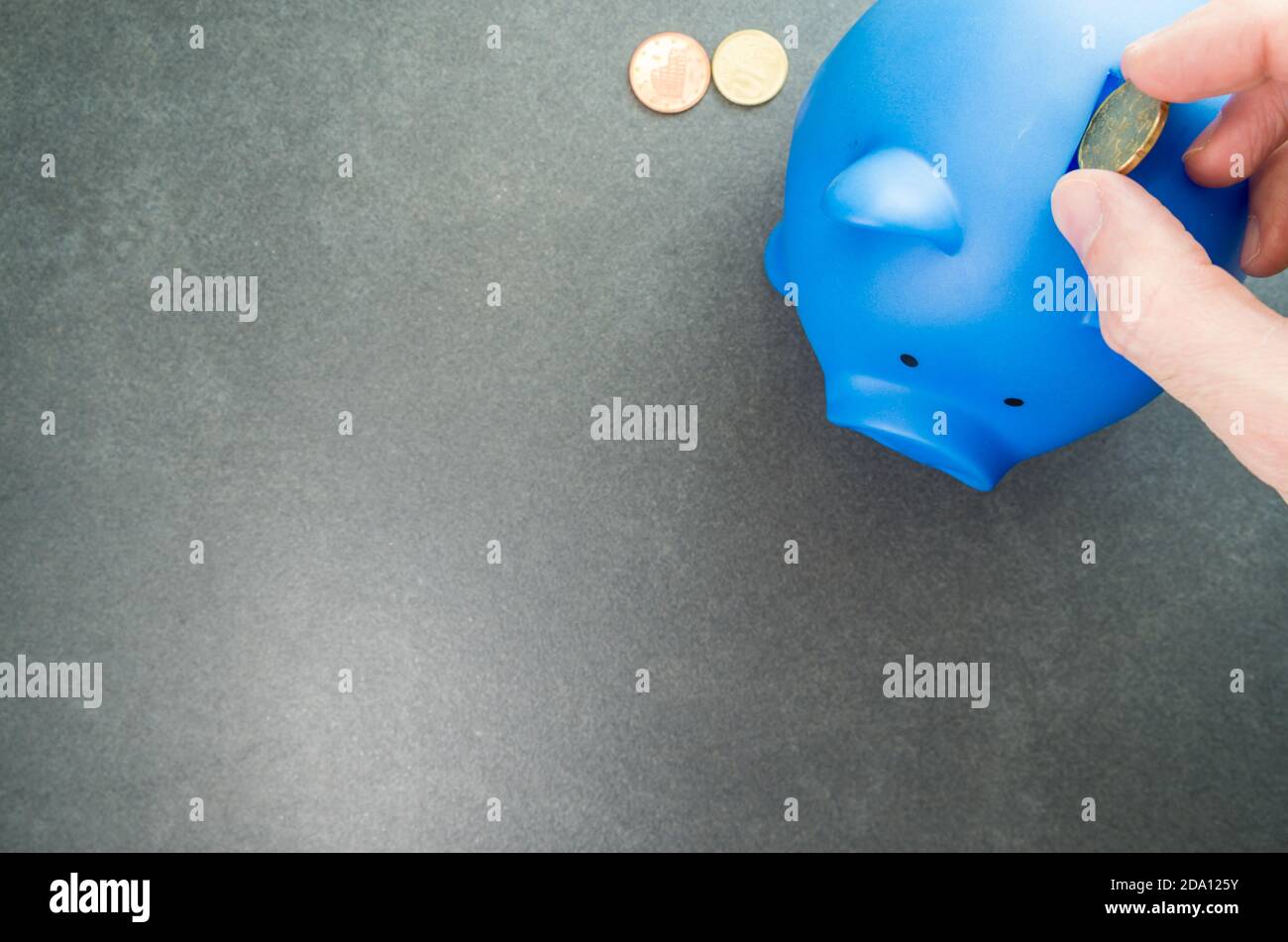 Top view of a hand adding a coin to a blue piggy bank Stock Photo - Alamy