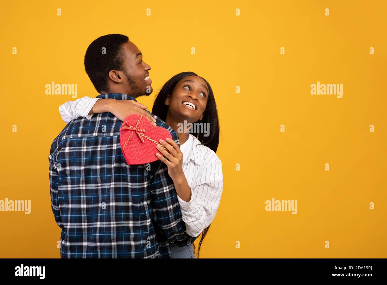 Smiling african american guy and lady hugging, look up at empty space ...