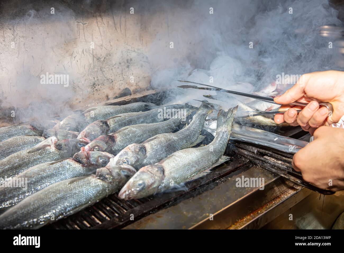 Grilled sea bass fish closeup. In process. European sea-bass, chef is ...