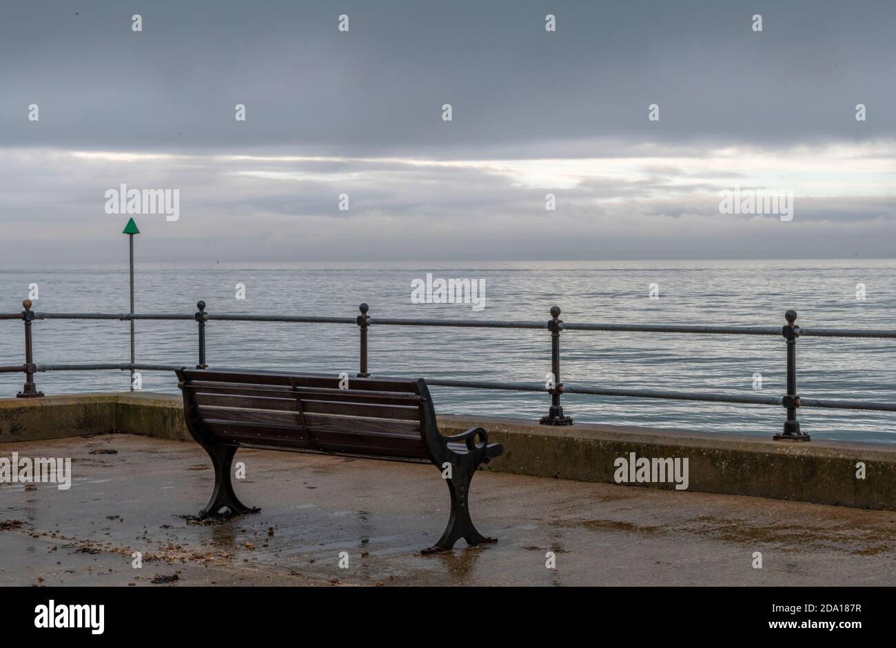 a empty wooden bench on the seafront in the rain on an overcast day ...