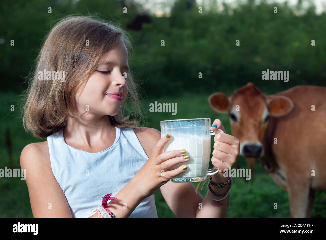 Smiling Teenage girl with a cup of fresh milk on the green pasture with ...