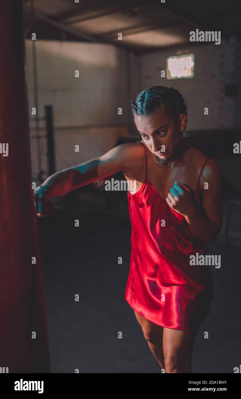 Shallow focus of an adult female in a red dress boxing on a punching ...