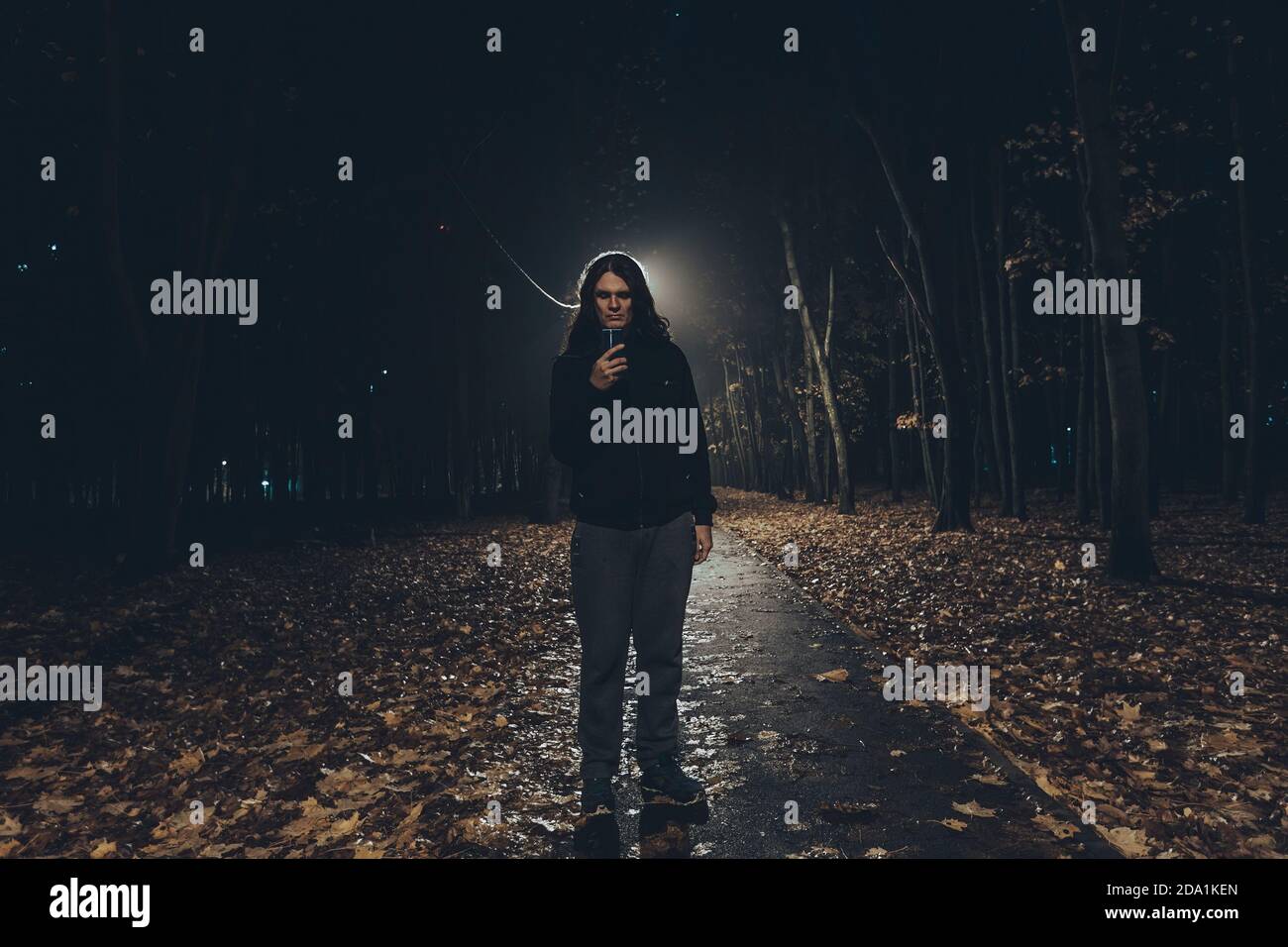 Sad man alone walking along the alley in night foggy park. Back view ...