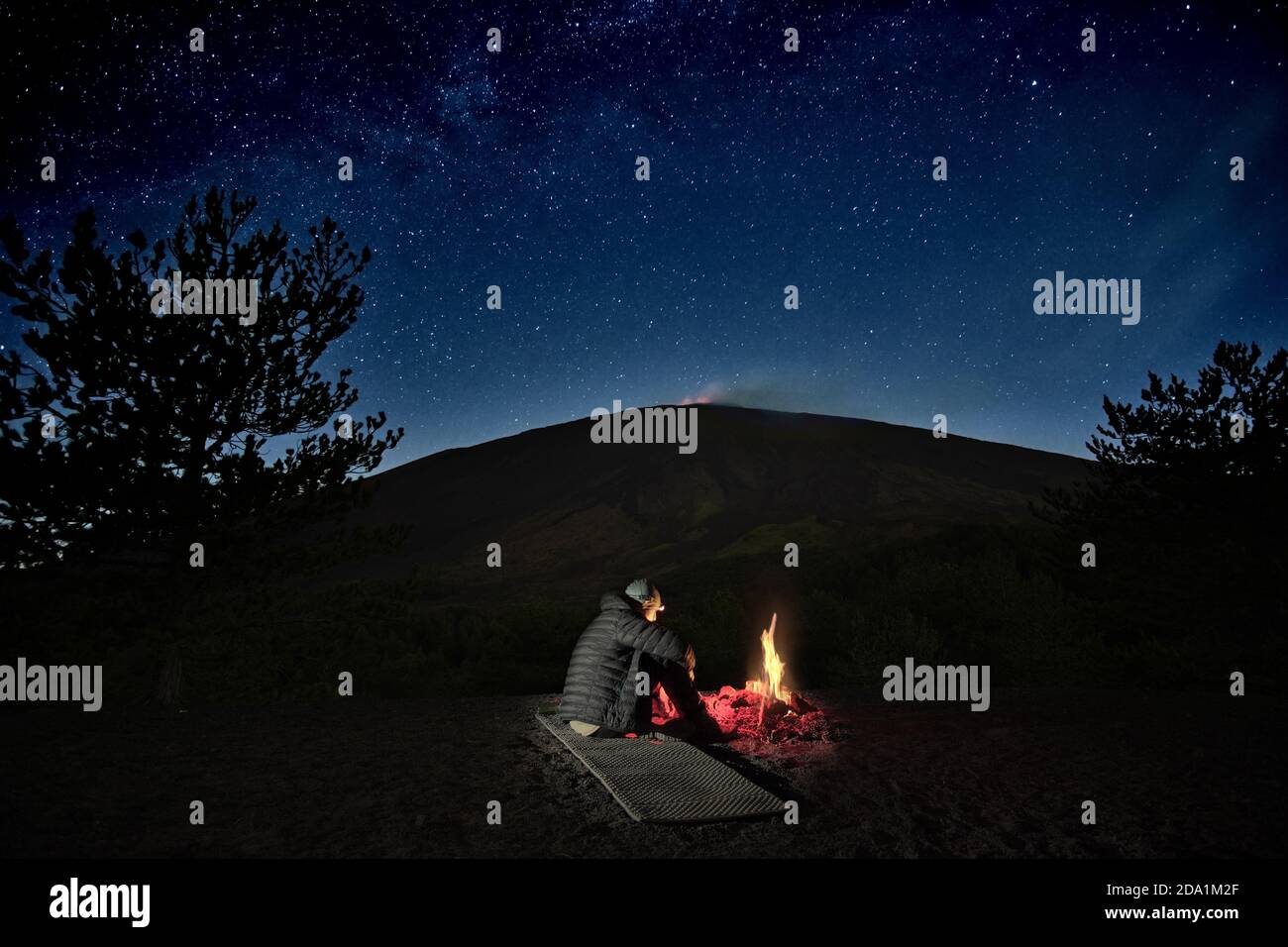 alone man resting by the campfire under Etna Volcano and starry sky ...