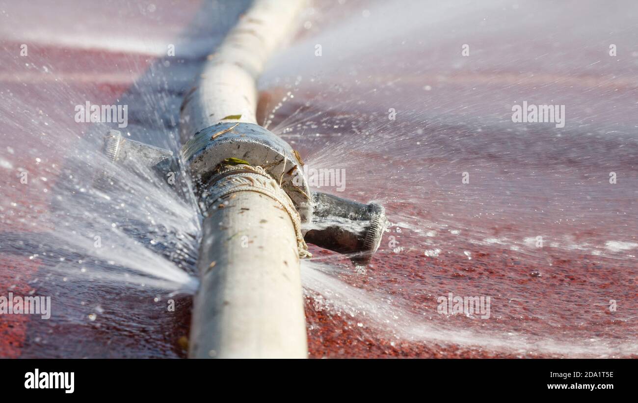 wasting water - water leaking from hole in a hose Stock Photo - Alamy
