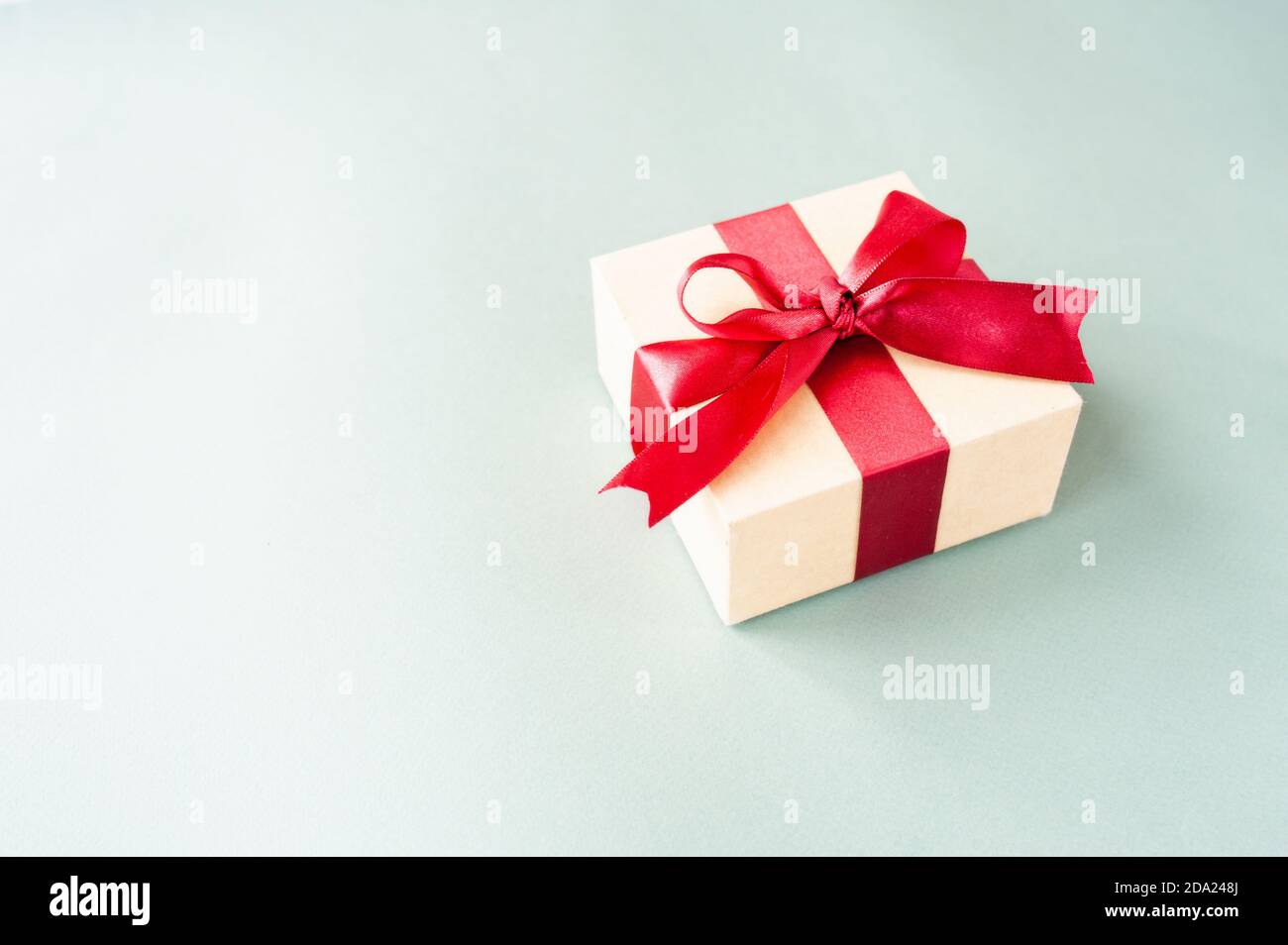 stylish square beige box with red festive satin ribbon on pastel blue ...