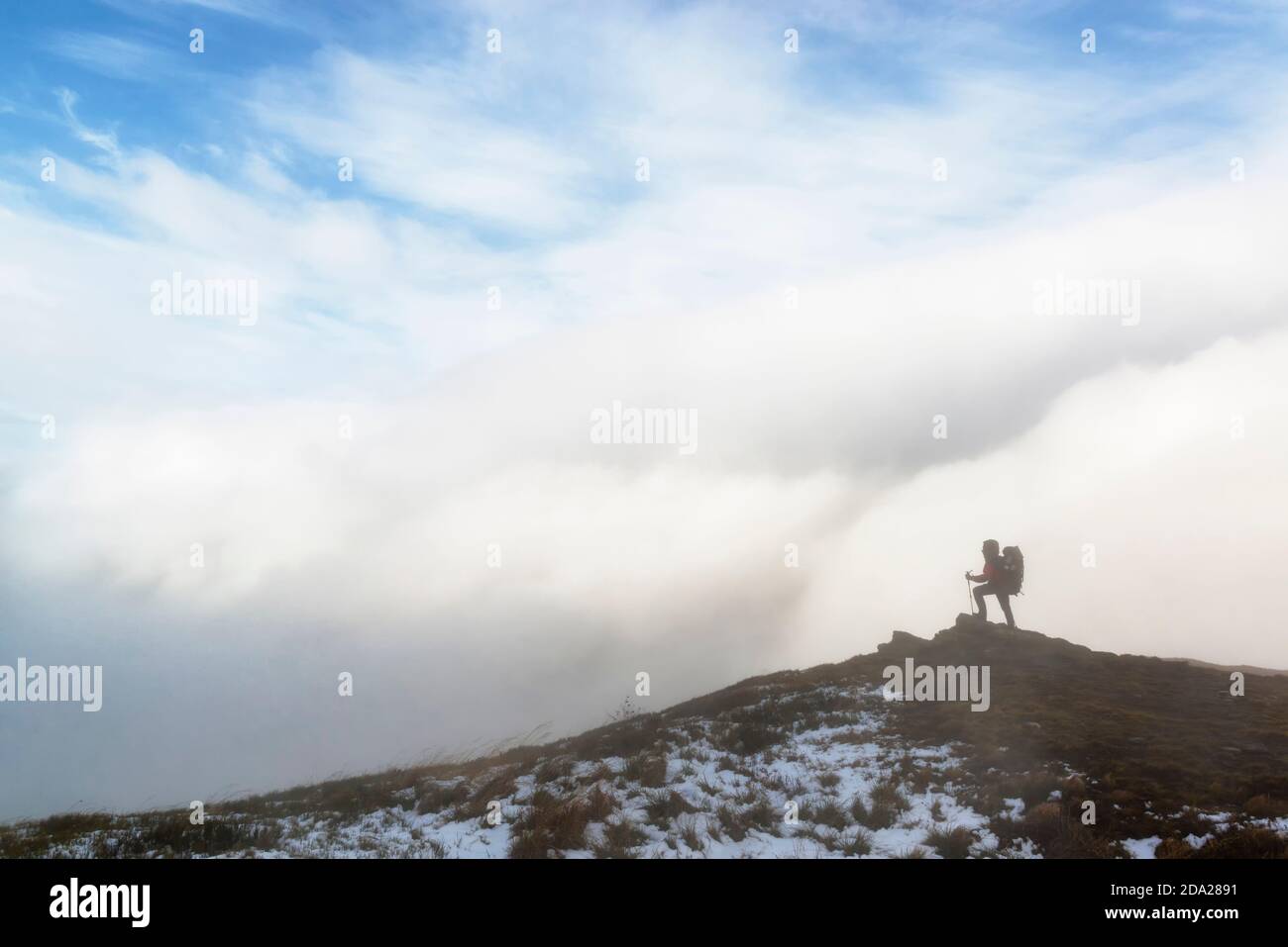 Hiker standing of the mountain top in front of dramatic clouds and ...
