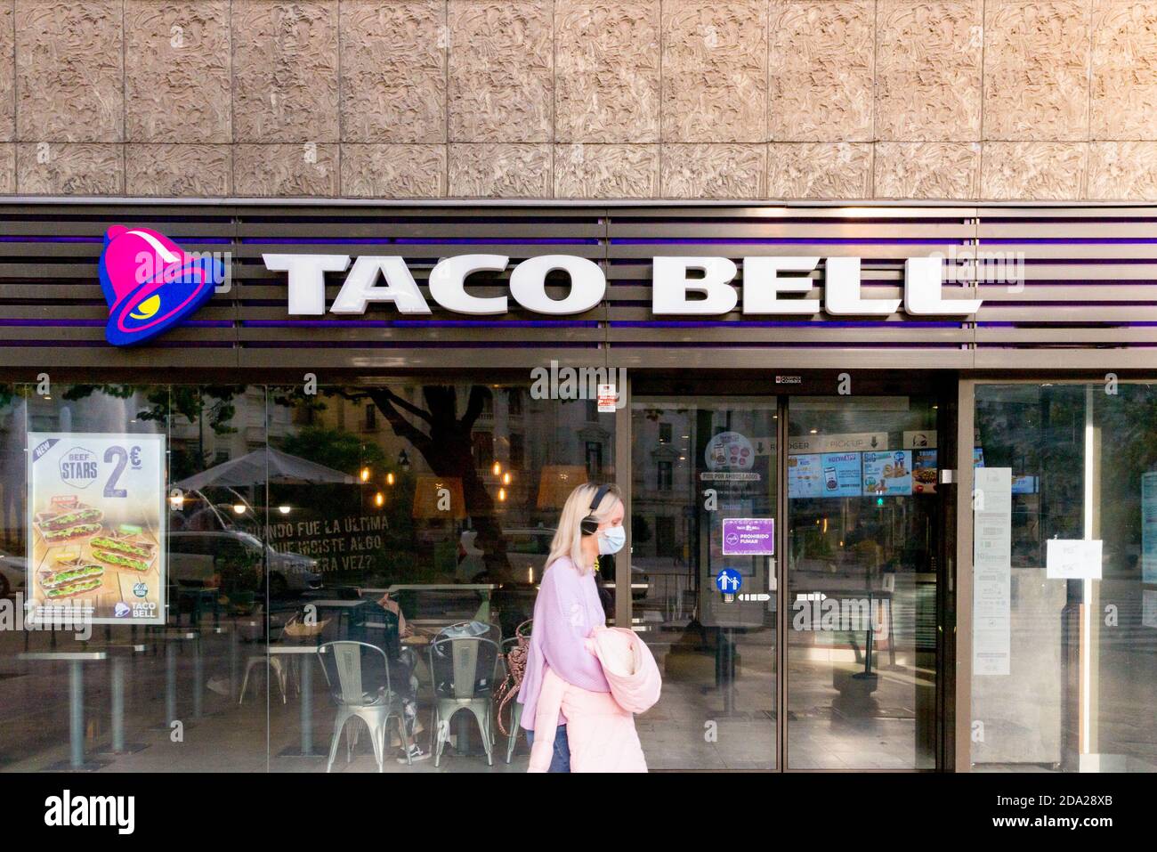 A woman wearing a face mask walks past a fast food restaurant Taco Bell ...