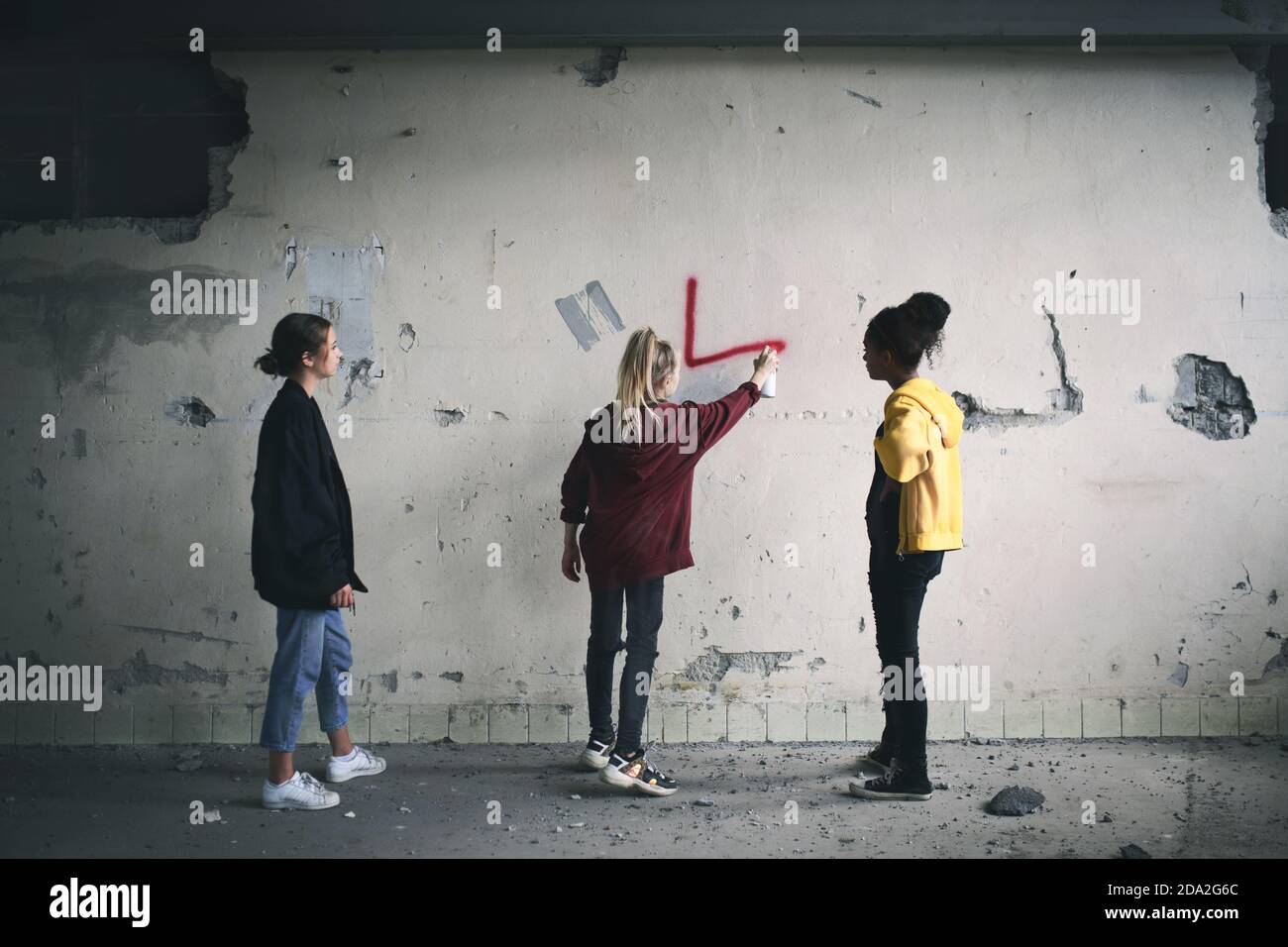 Rear view of group of teenagers girl gang standing indoors in abandoned ...