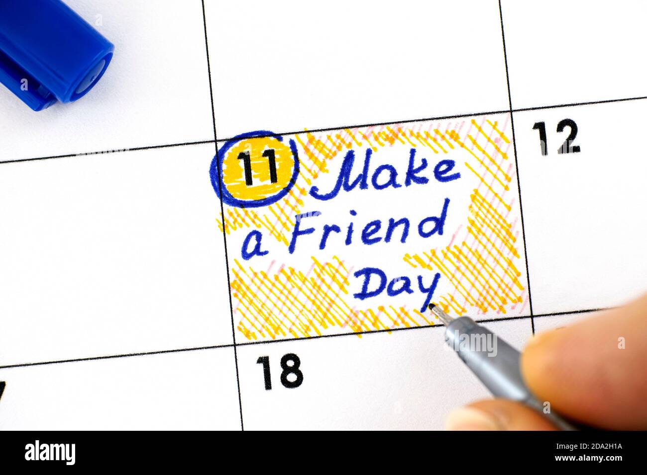 Woman fingers with pen writing reminder Make a Friend Day in calendar ...