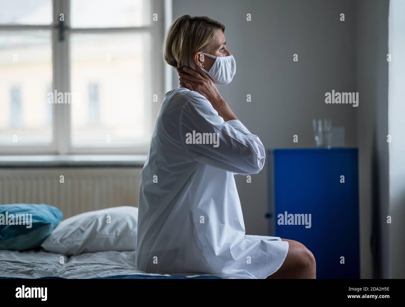 Woman patient with face mask sitting on bed in hospital feeling ...