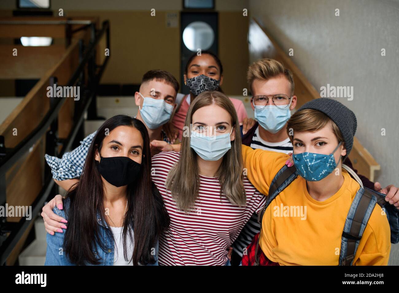 Front view of young students with face masks back at college or ...