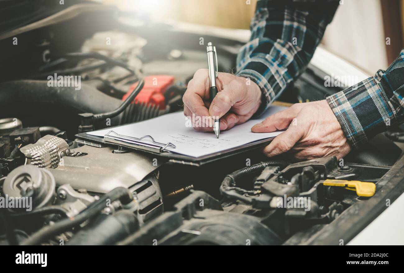 Car mechanic checking a car engine and writing on clipboard Stock Photo ...