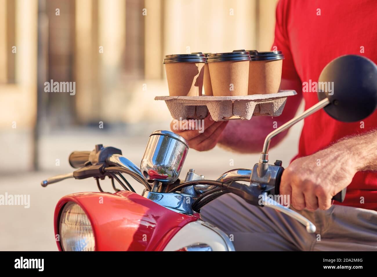 Male courier delivering four coffee cups on scooter, standing on a ...