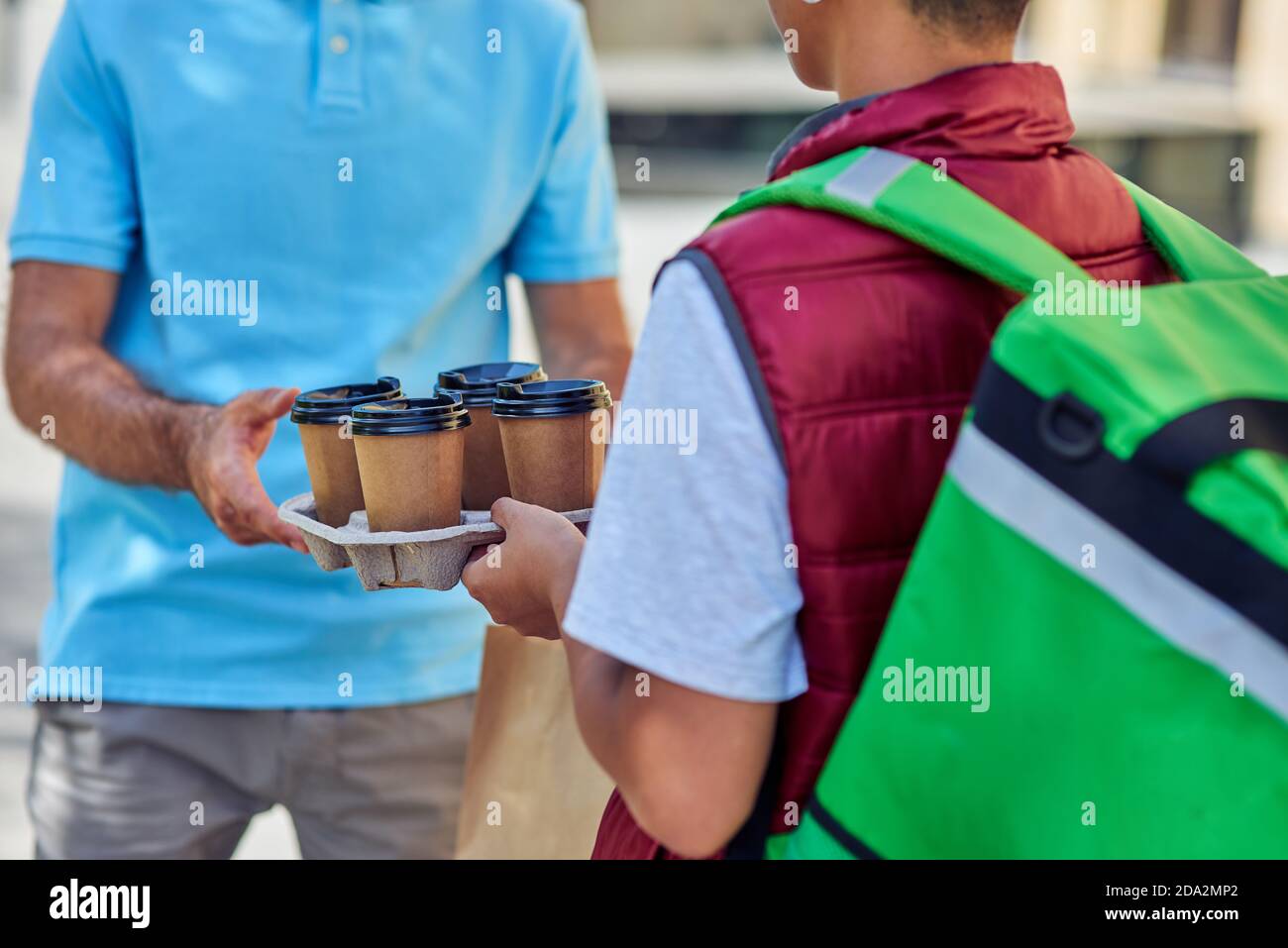 Male courier with thermo bag delivering four coffee cups to customer ...