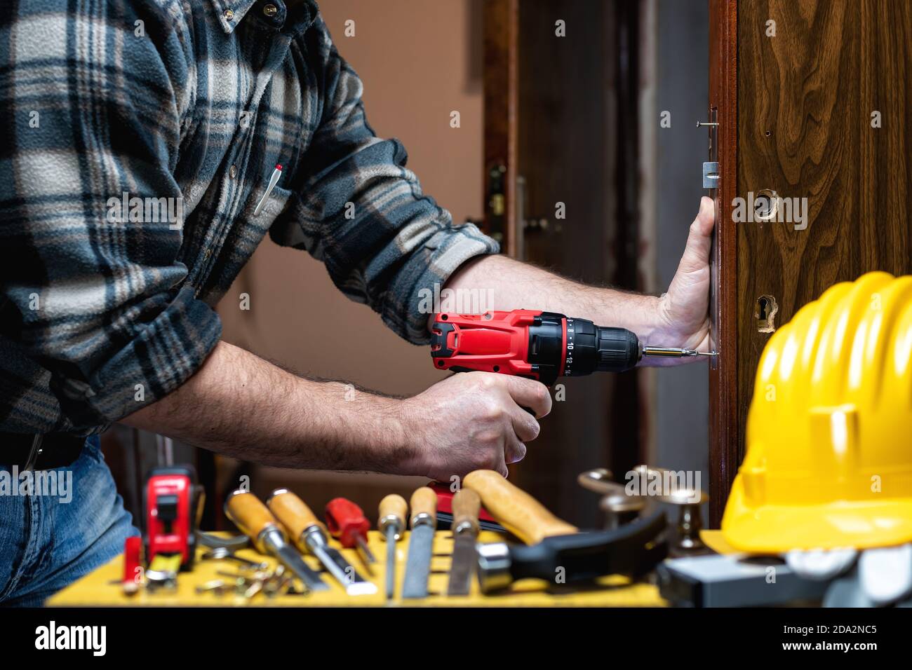 Close-up. Carpenter with an electric screwdriver fixes the lock of a ...