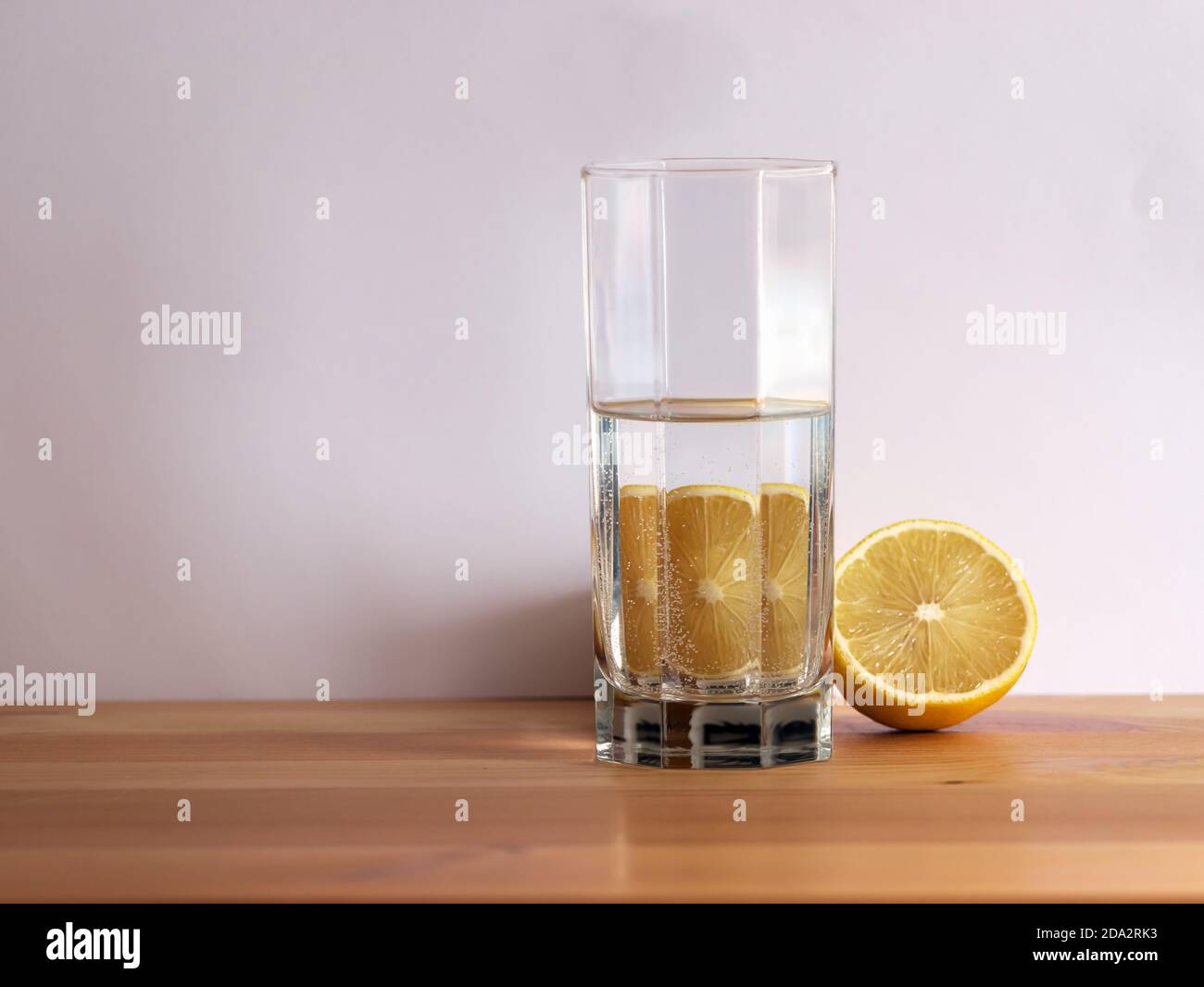 Glass of water and cut lemon is standing on the wooden desk. White ...