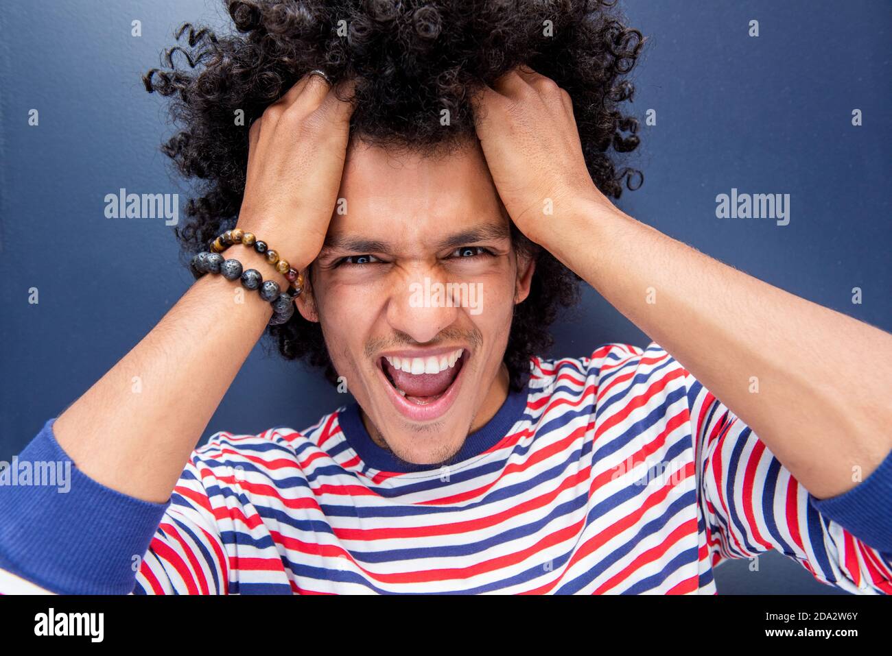 Close up portrait young arabic man screaming with hands in hair by blue ...