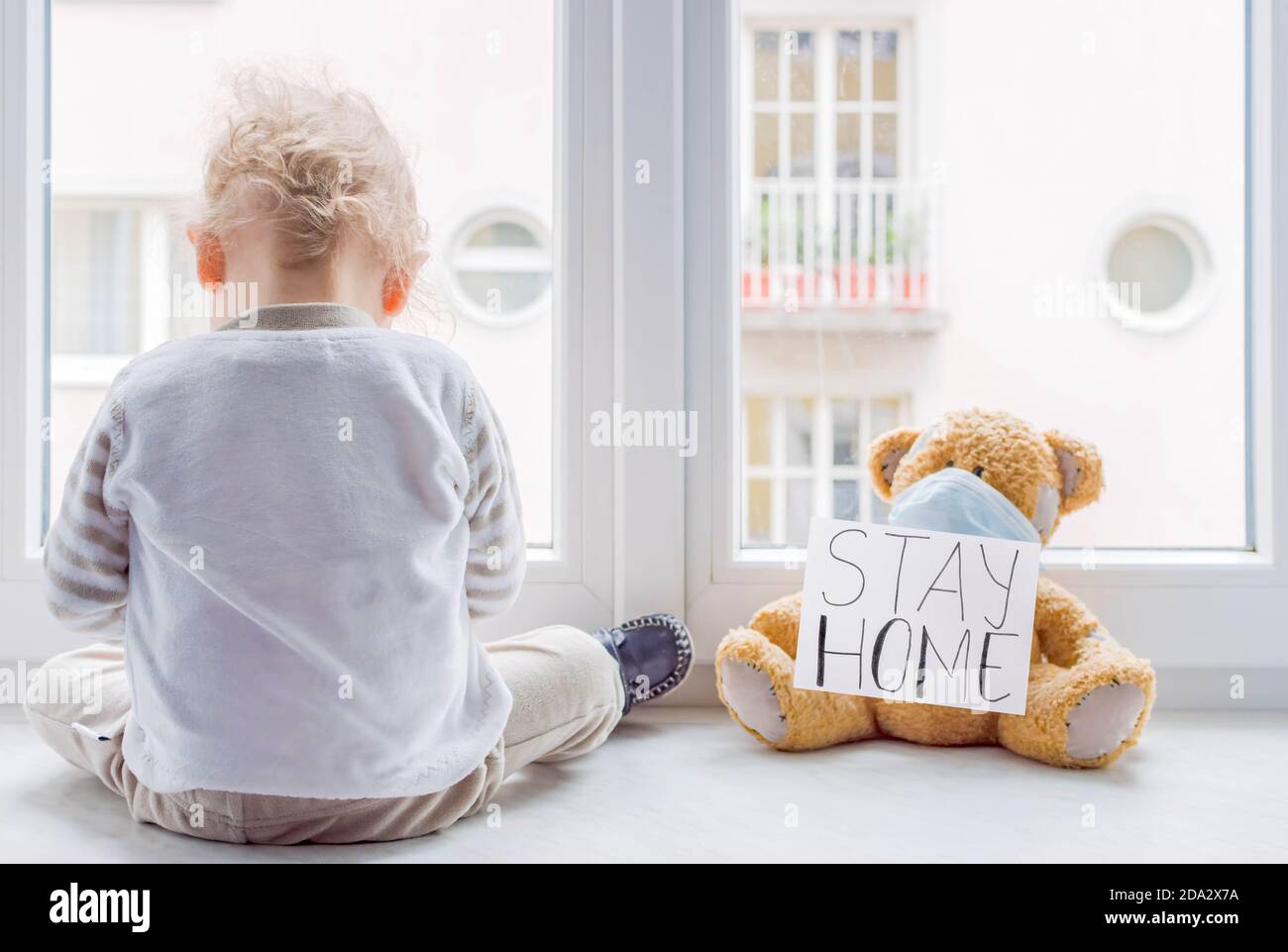 Child in home quarantine playing at the window with his sick teddy bear ...