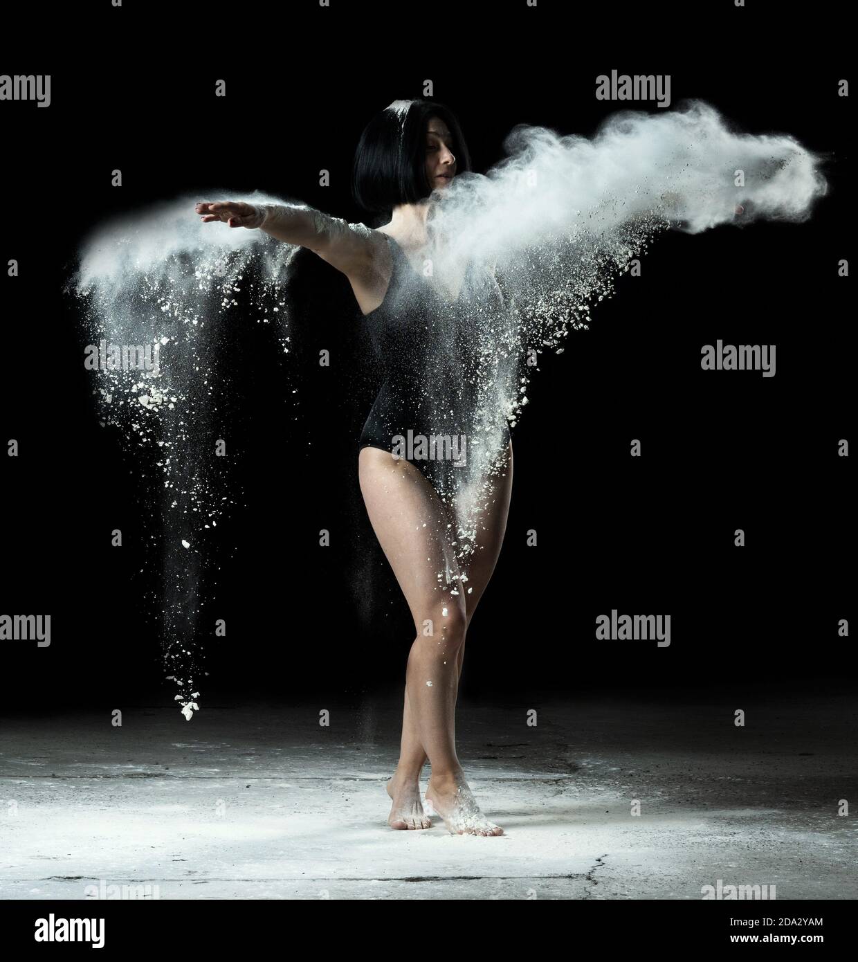 woman with athletic figure dancing in flying white flour on black ...