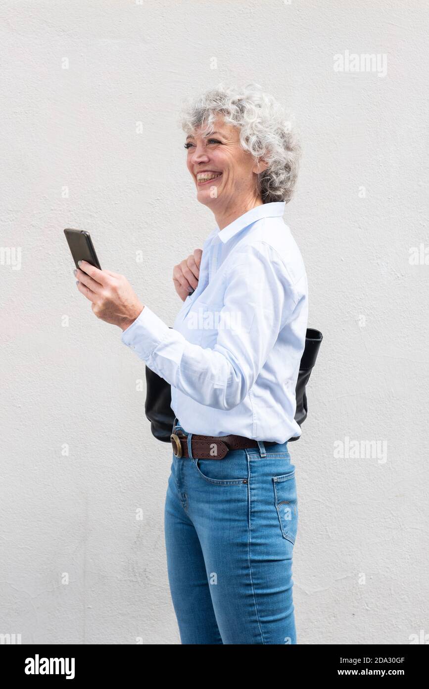 Side portrait middle aged woman holding mobile phone by white ...