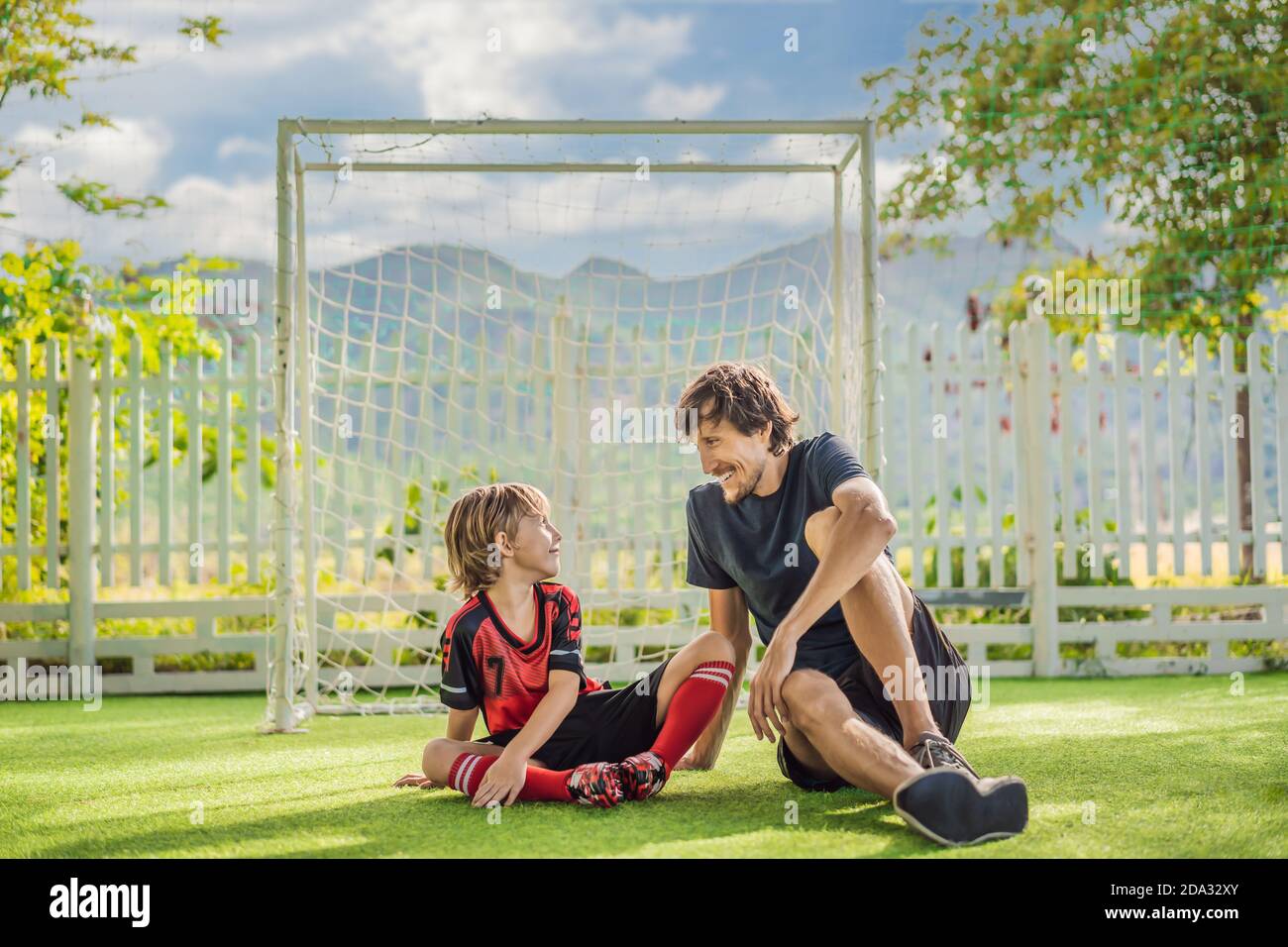 Little cute kid boy in red football uniform and his trainer or father ...