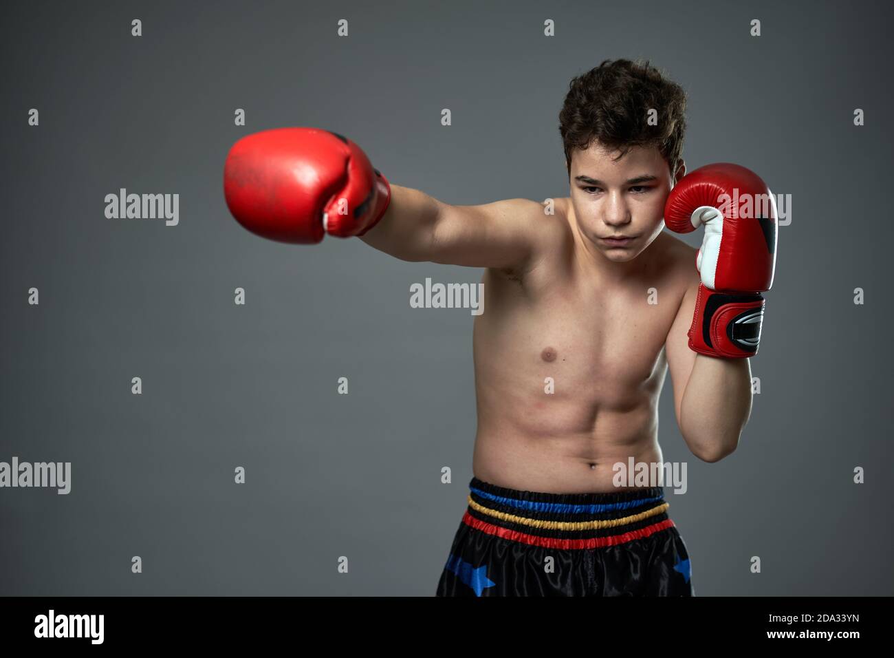 Young boxer with red gloves striking various poses on gray background ...