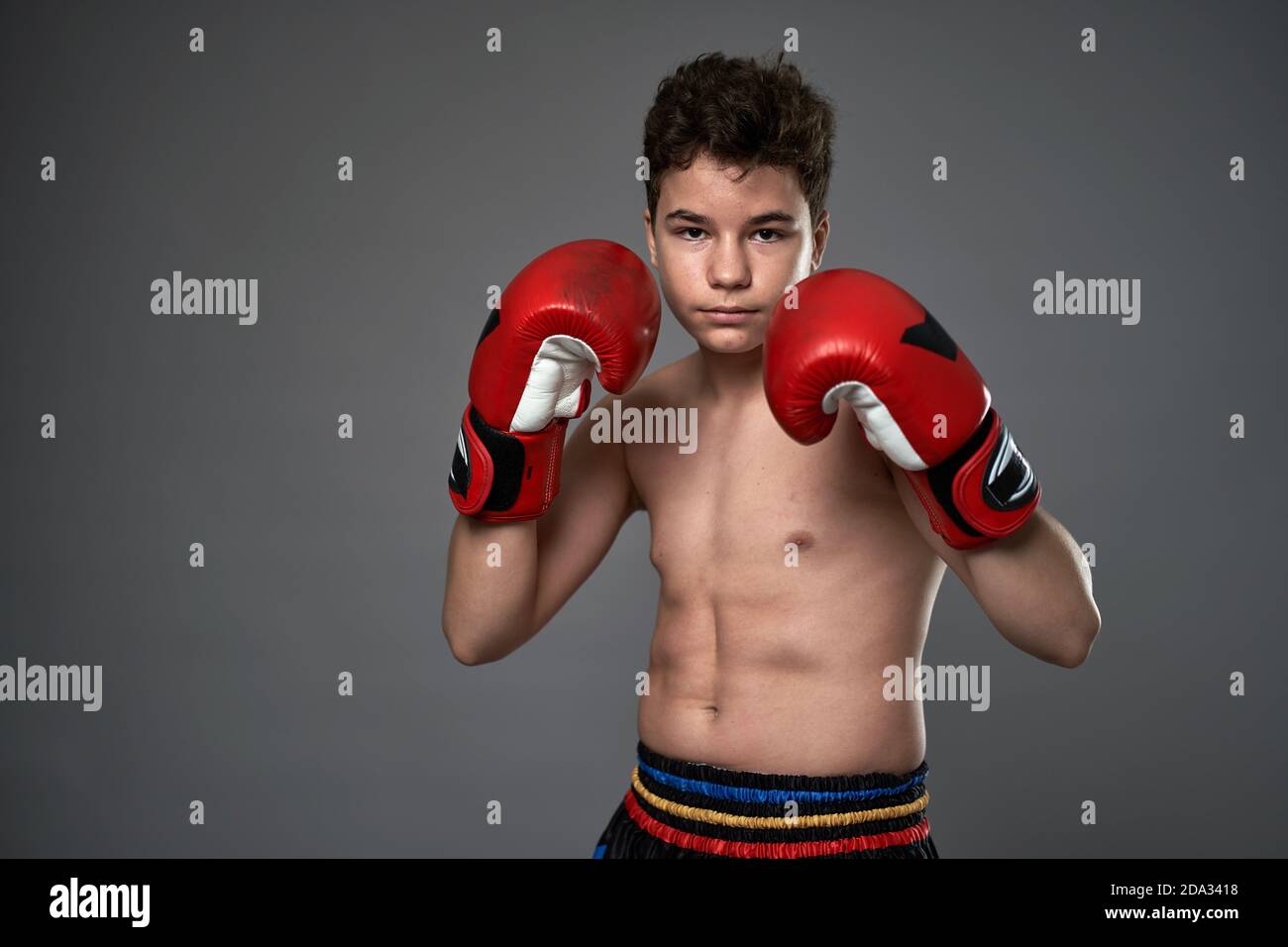 Young boxer with red gloves striking various poses on gray background ...