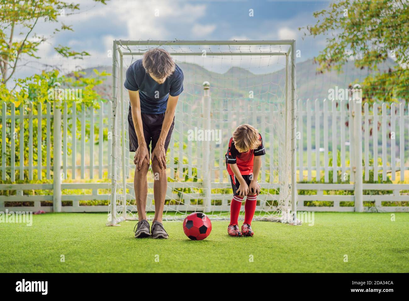 Little cute kid boy in red football uniform and his trainer or father ...