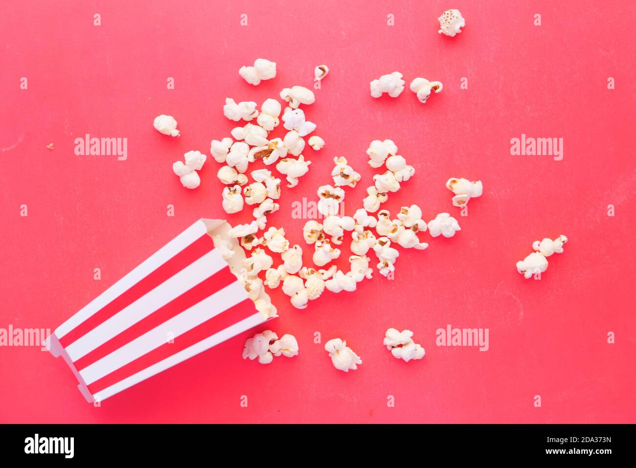 popcorn spilling from a container on red background Stock Photo - Alamy