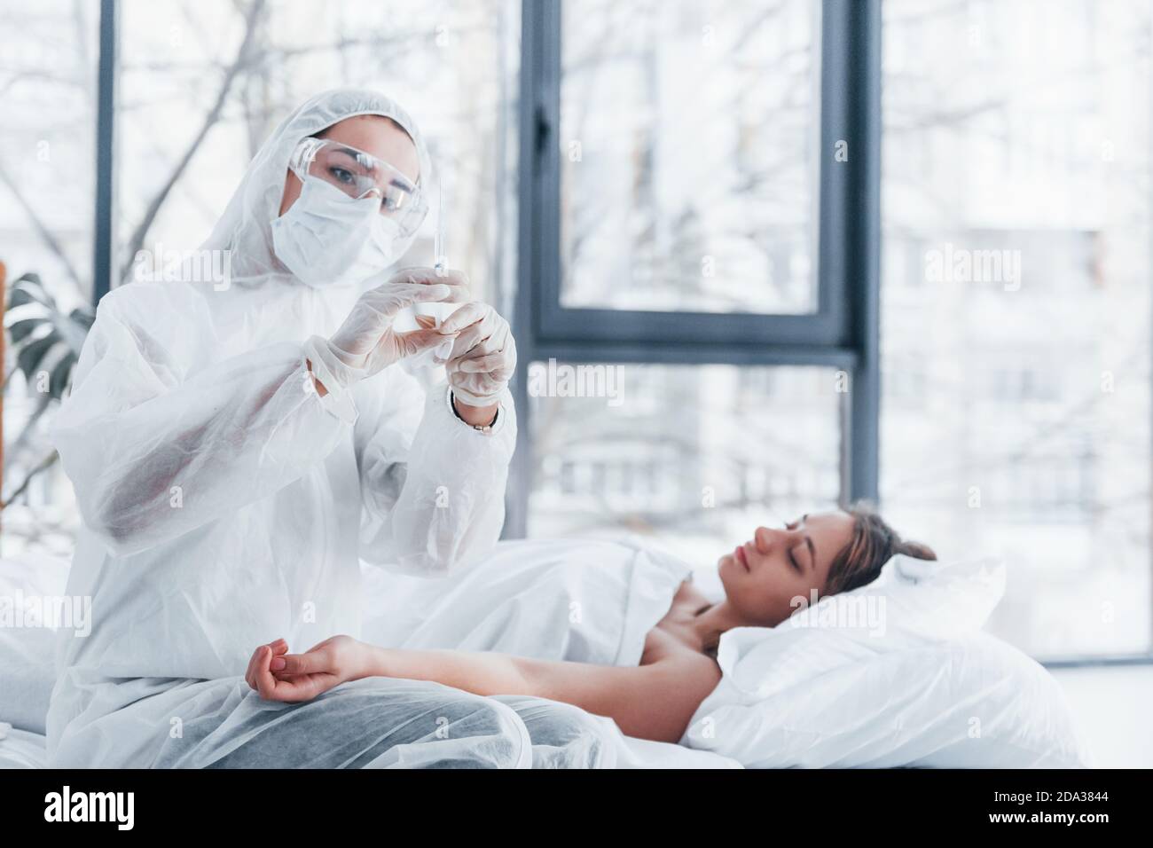 Female doctor in defensive lab coat and protective eyewear with syringe ...