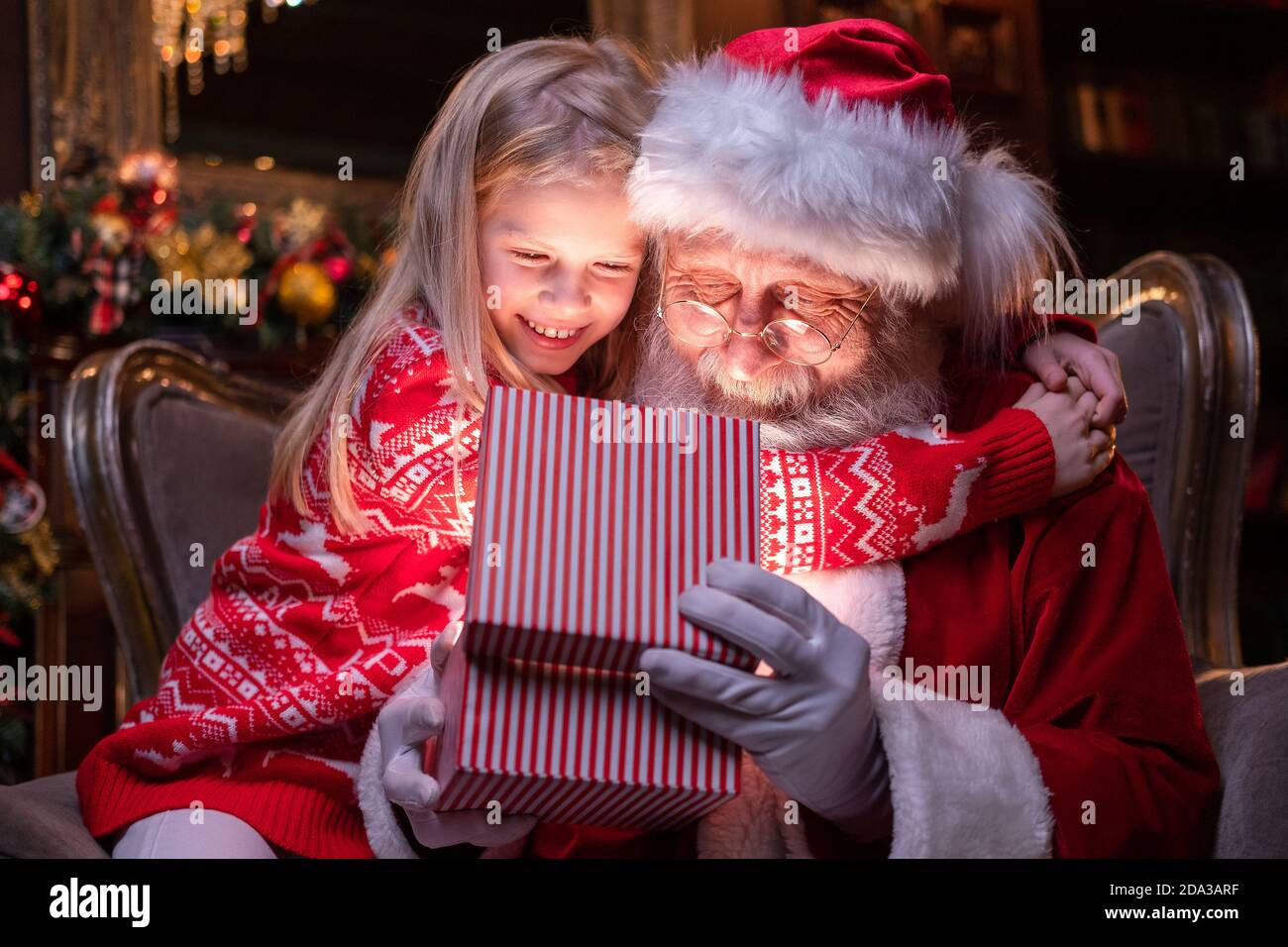 Santa Claus and girl opening Christmas gift near Christmas tree. Child ...