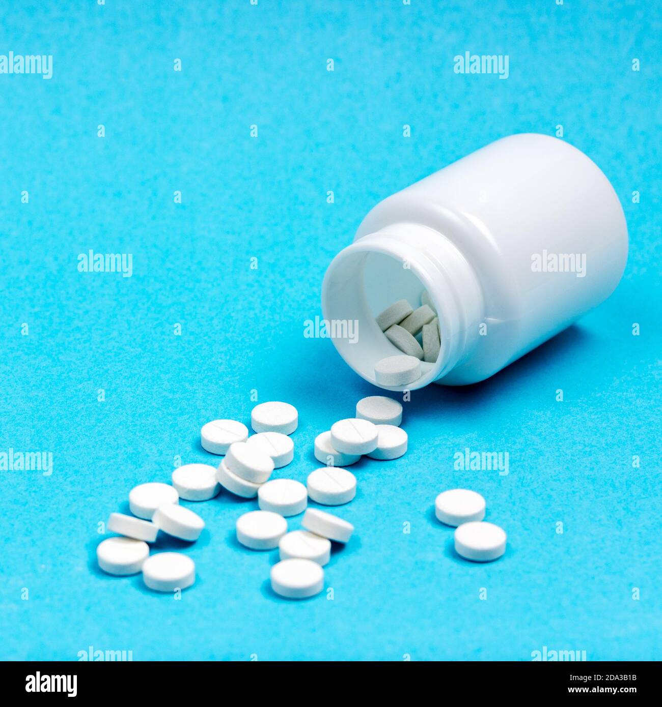White pharmaceutical pills and white inverted jar on a light blue ...