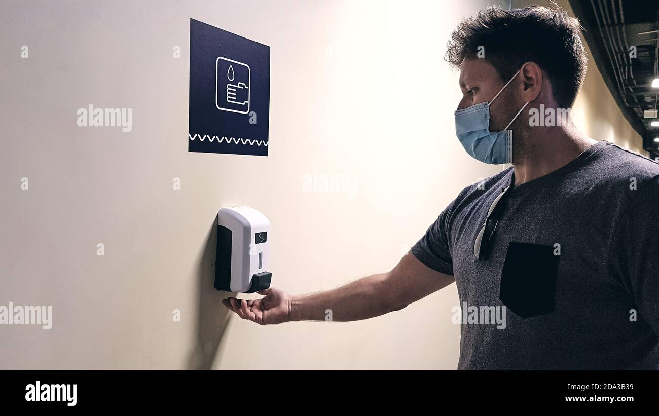 Man wearing protective face mask uses automatic hand sanitizer ...
