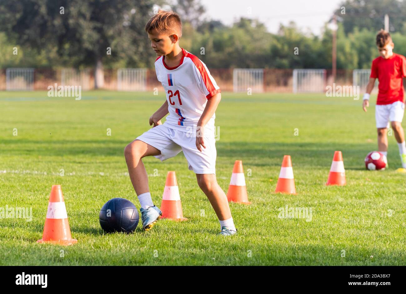 boy in sportswear trains football on soccer field and learns to circle ...