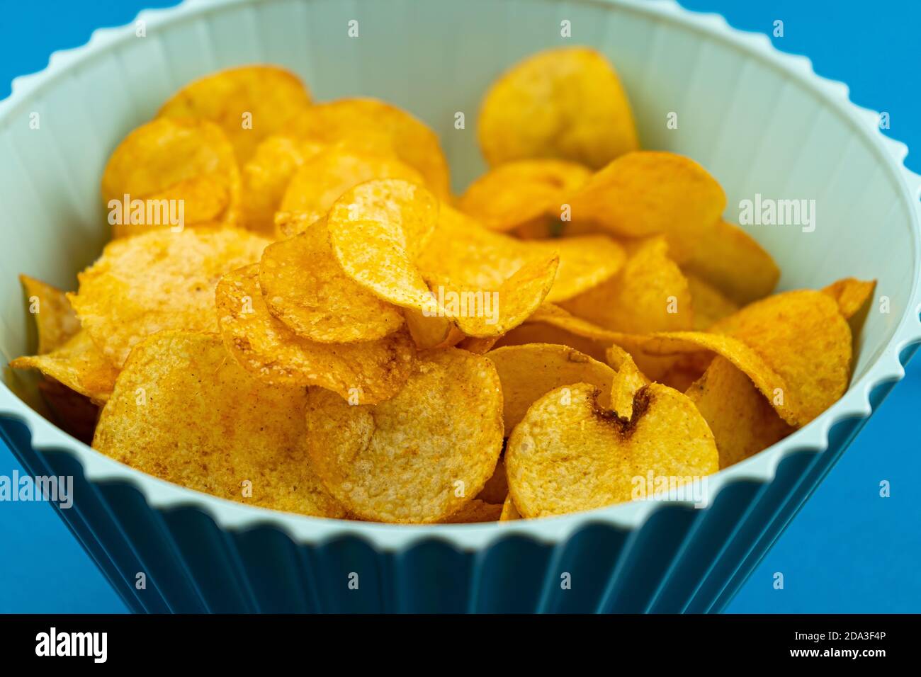 A bowl of potato chips on a blue background with copy space. Party ...