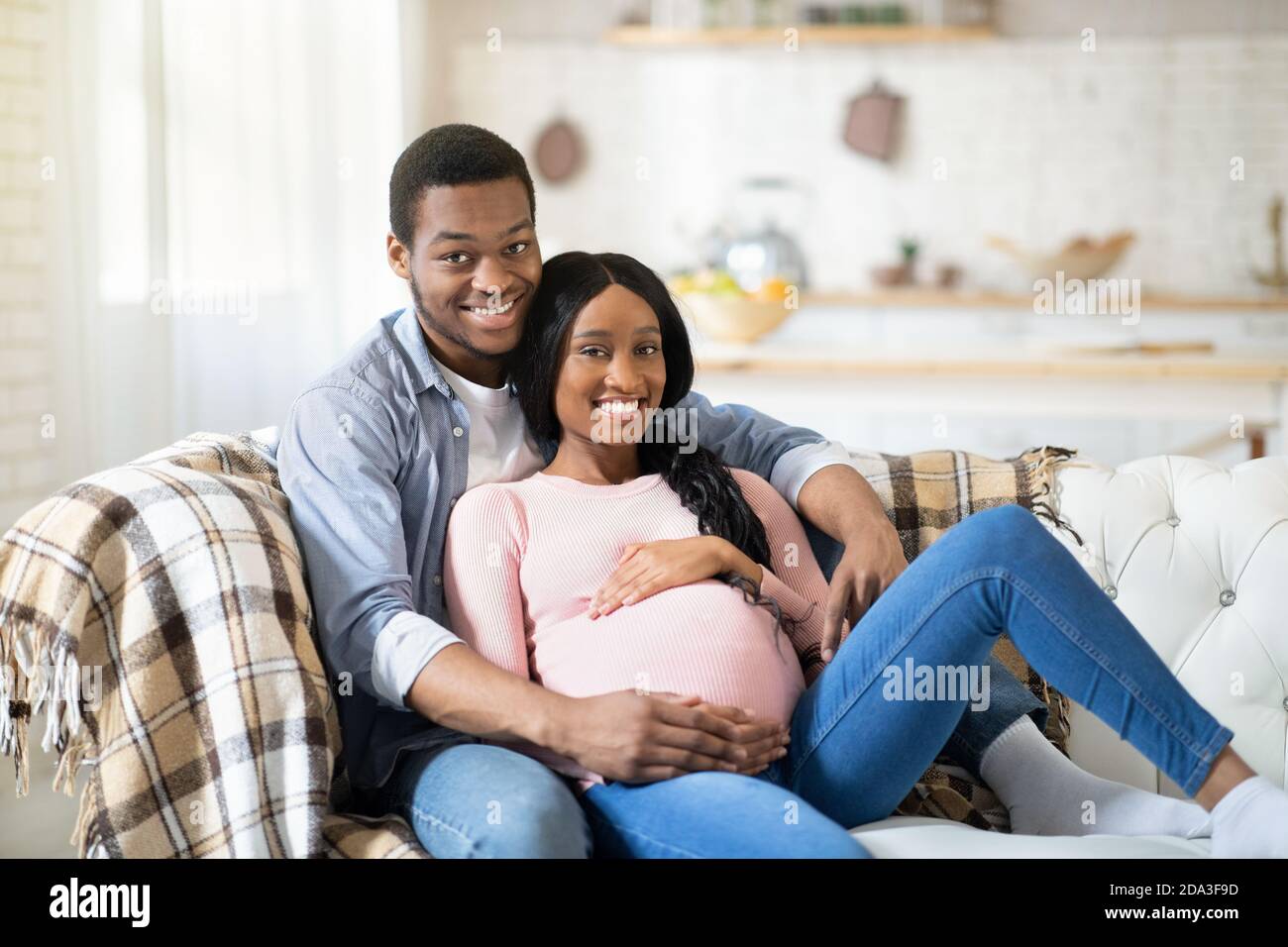 Beautiful pregnant couple hugging on sofa at home Stock Photo - Alamy