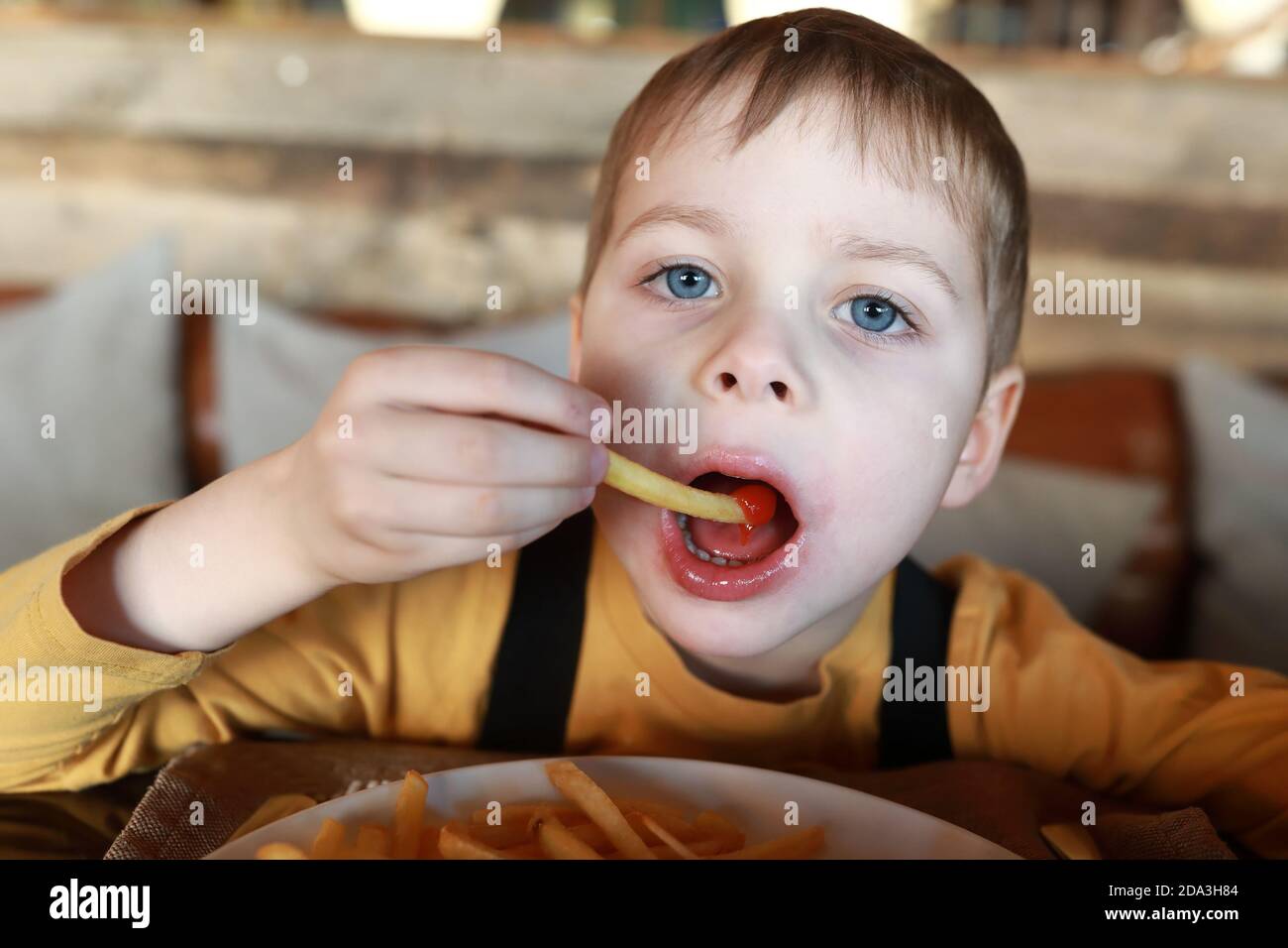 Boy eats french fries with ketchup in restaurant Stock Photo - Alamy