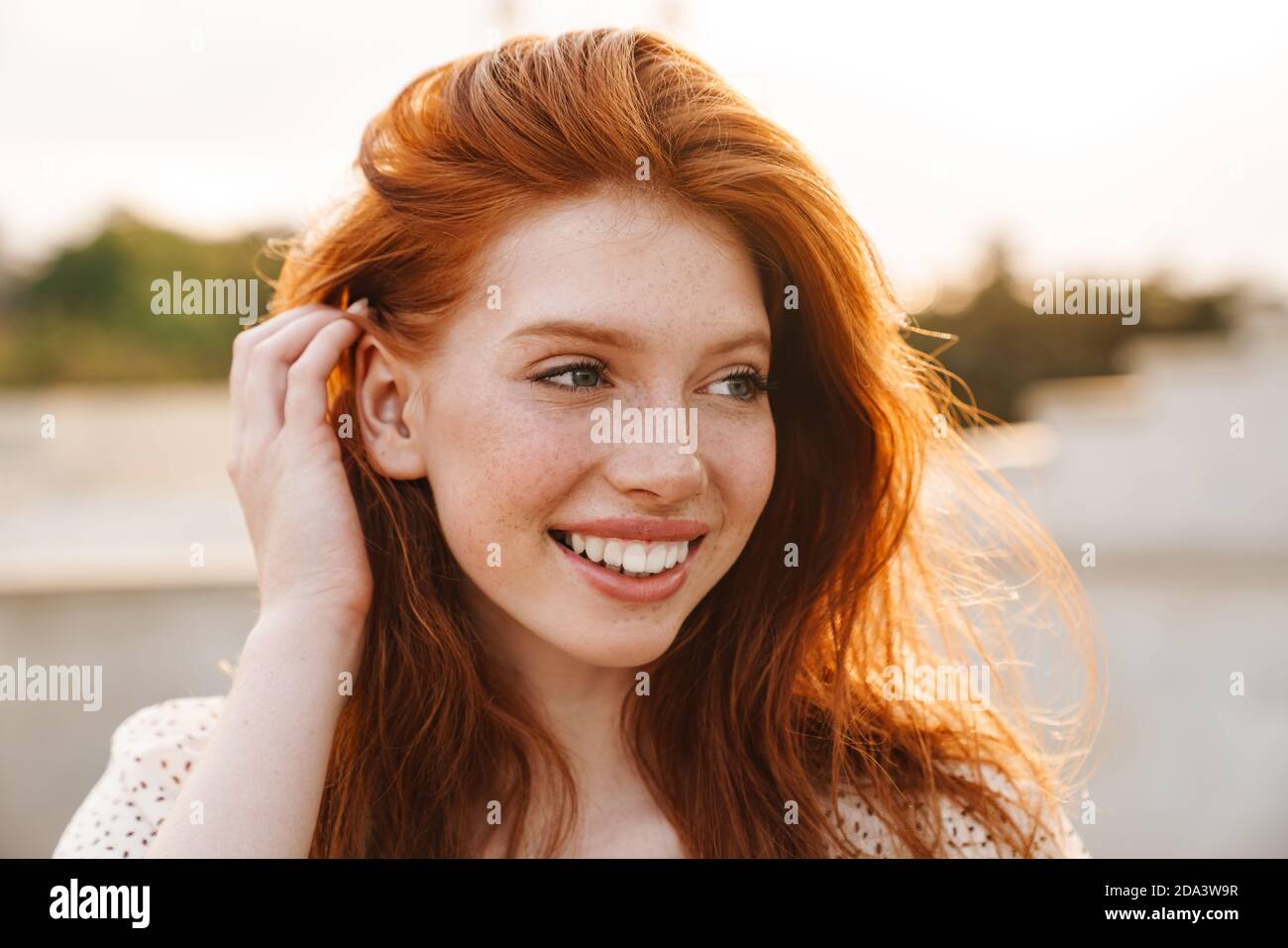 Image of cheerful ginger girl smiling and looking aside at city street ...