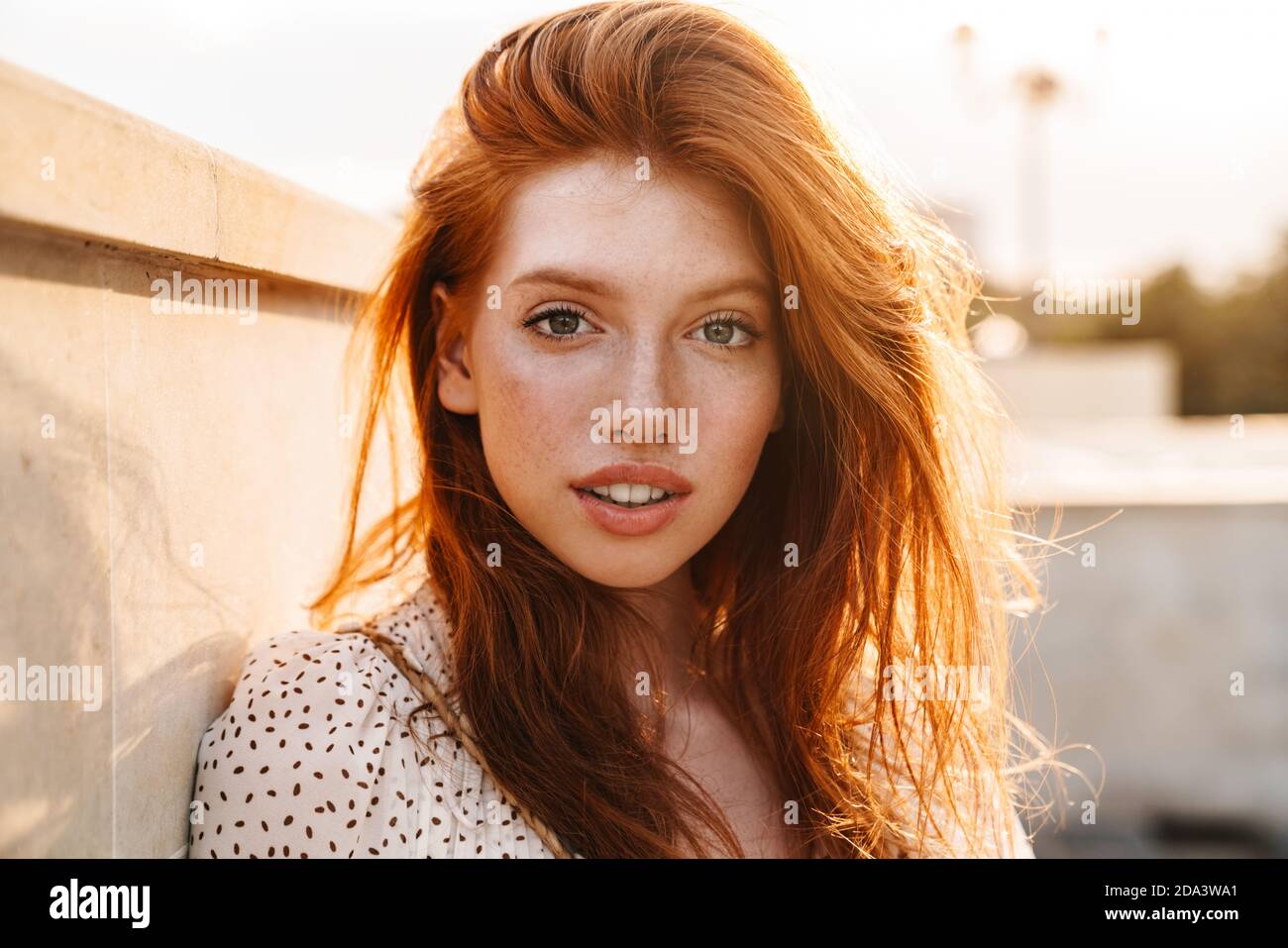 Image of pleased ginger girl posing and looking at camera at city ...