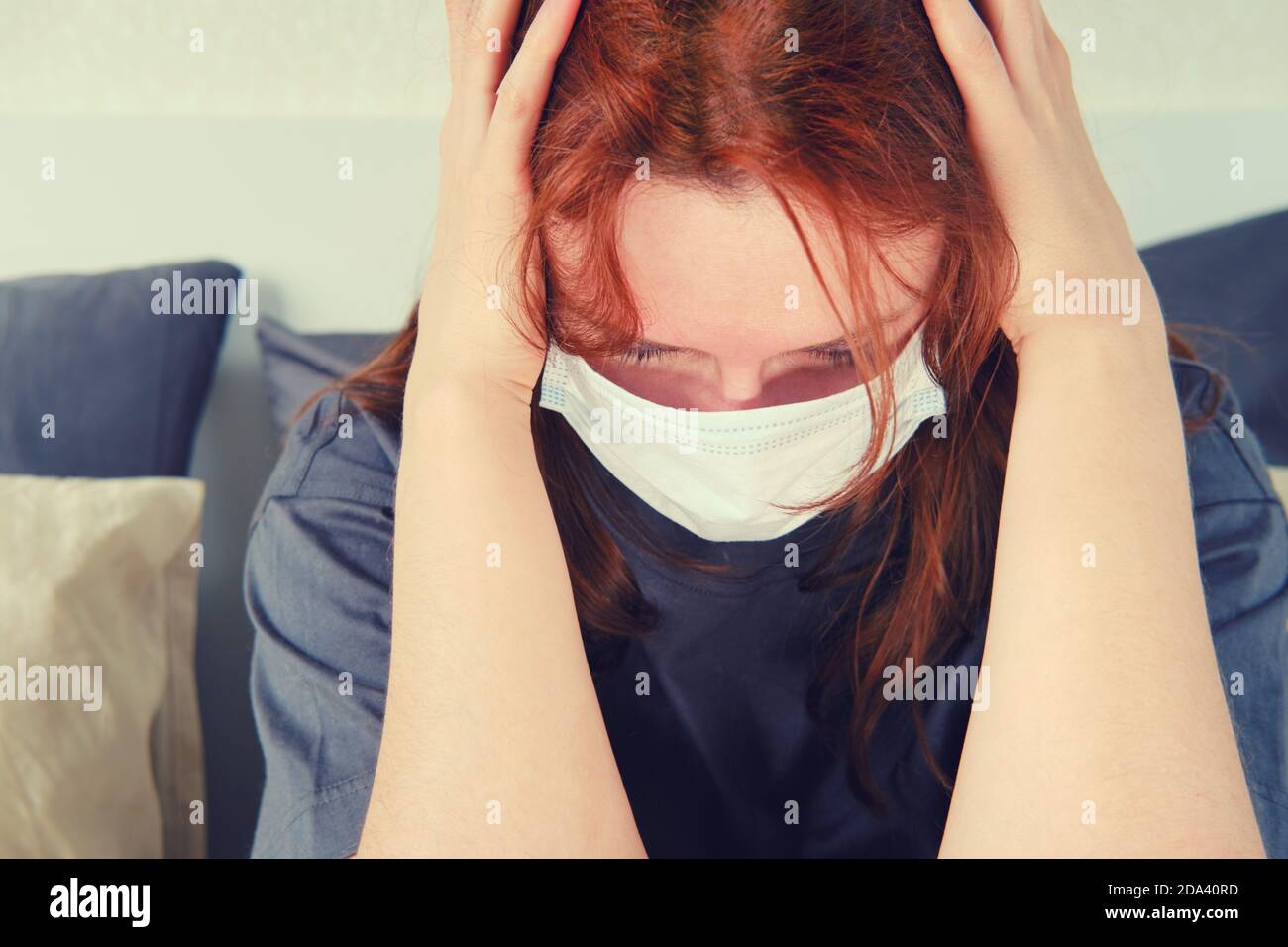 A woman in a medical mask has a headache. Girl with a sore head sits on ...