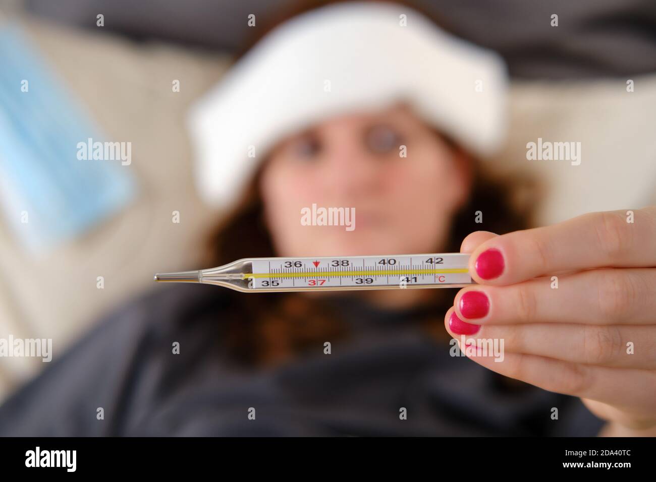 Woman shows the measured temperature lying in bed with a thermometer ...