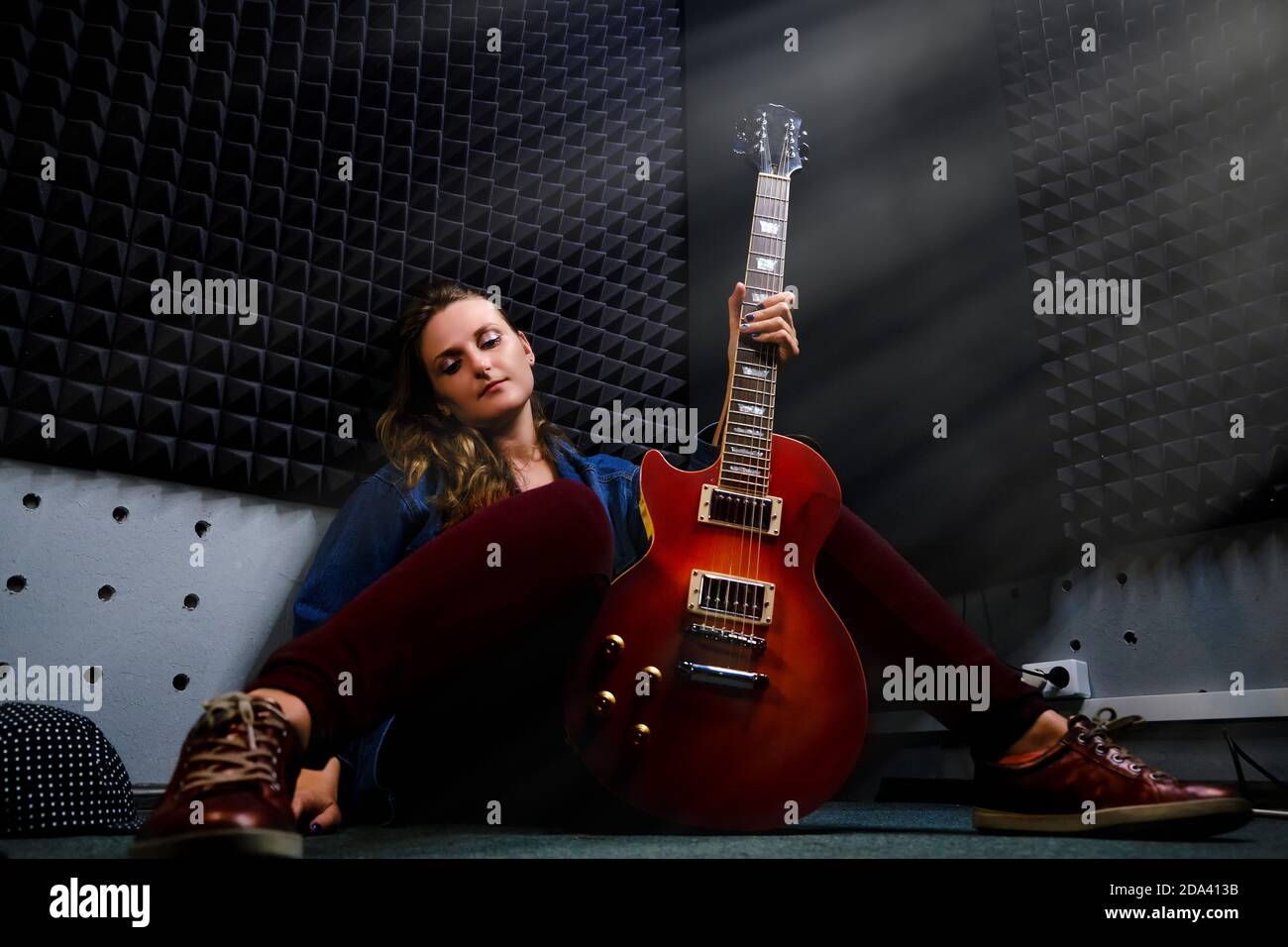 Woman put a red electric guitar in her feet. Denim jacket, cap, jeans ...