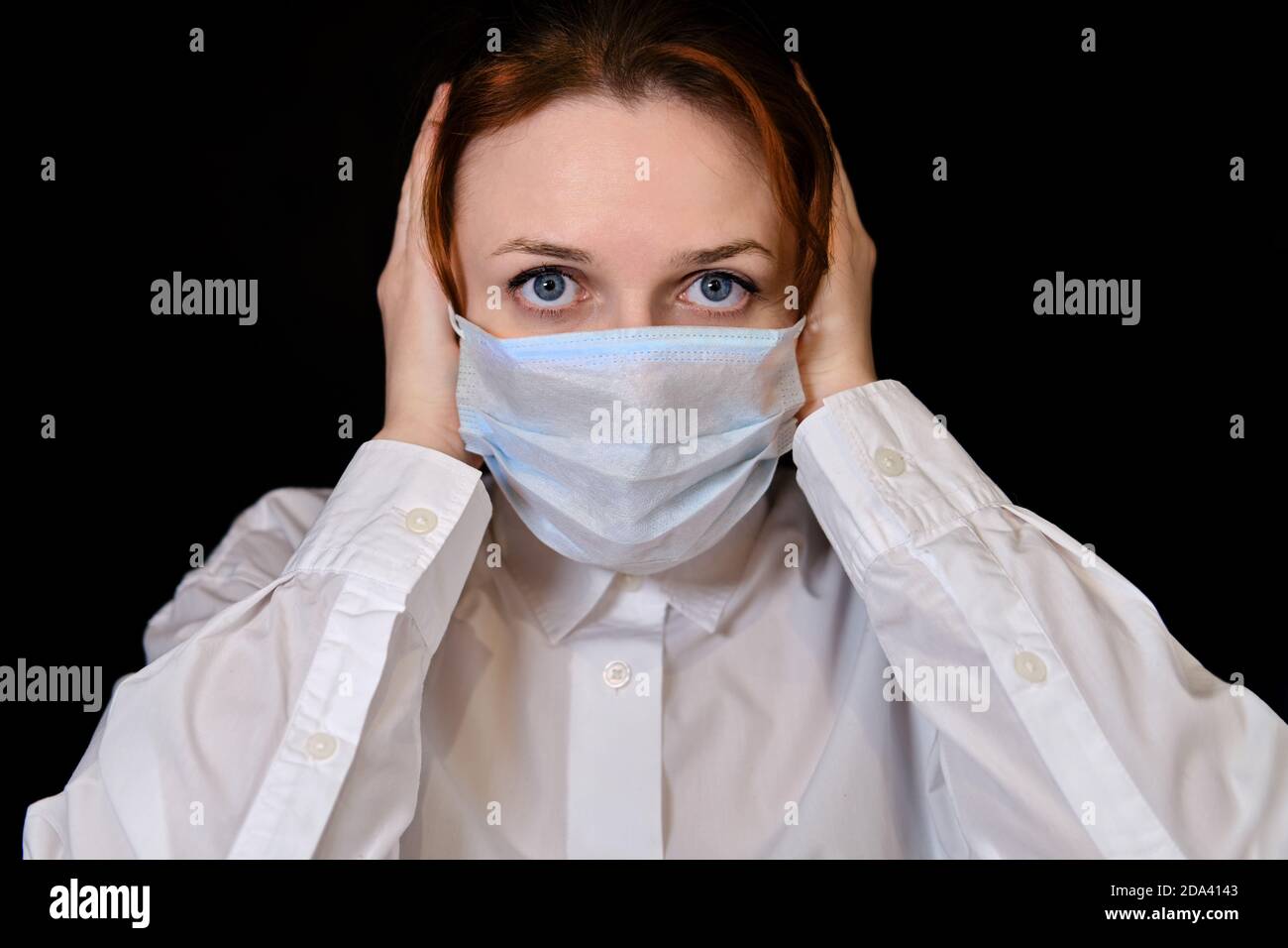 A woman with a scared look in a medical mask on a black background. The ...