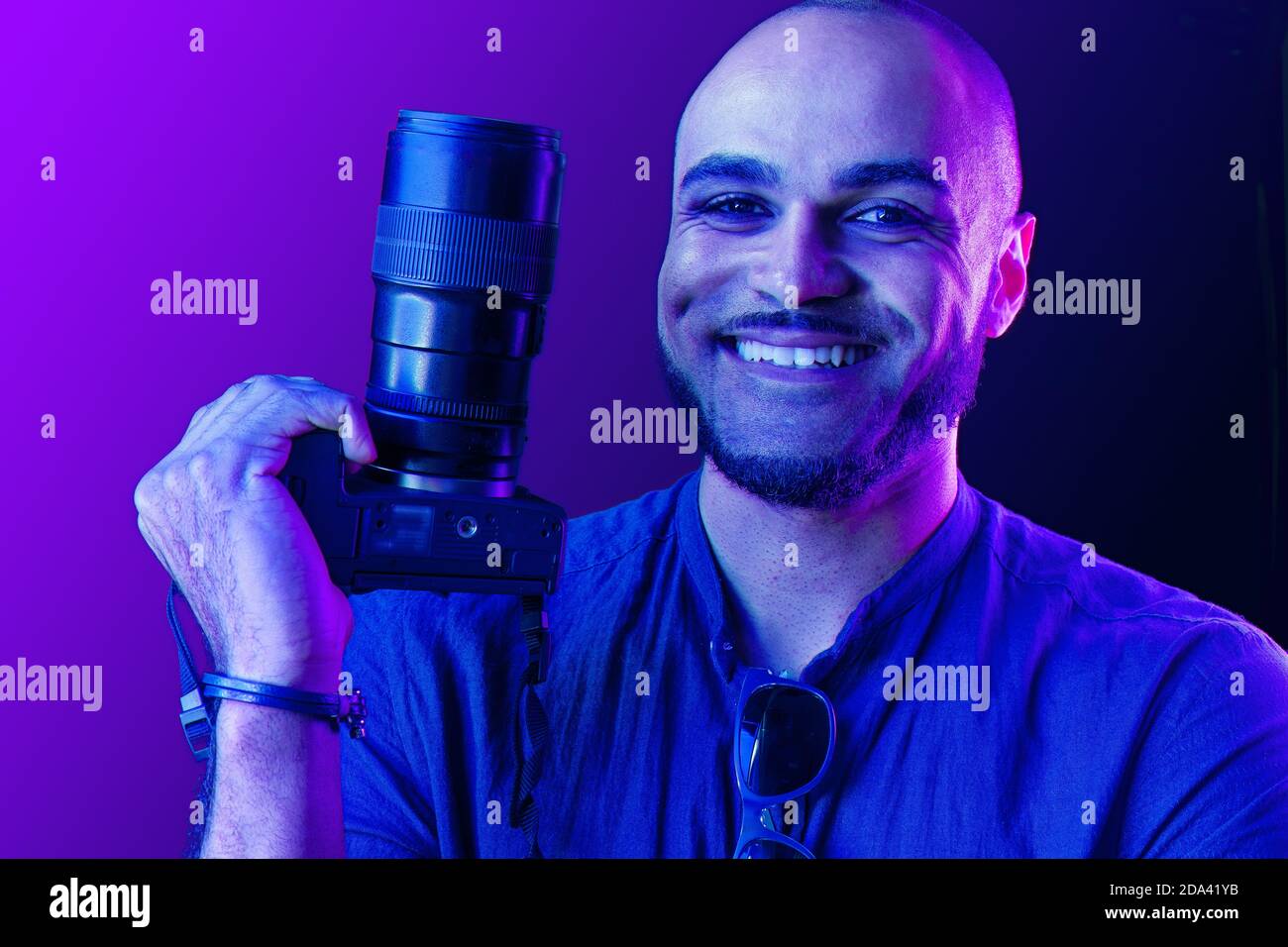 Black man with camera standing against purple background in neon light ...