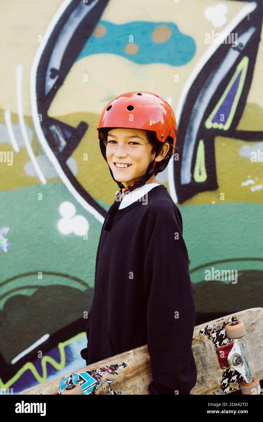 Portrait of a young skater boy with an old skateboard and a red helmet ...