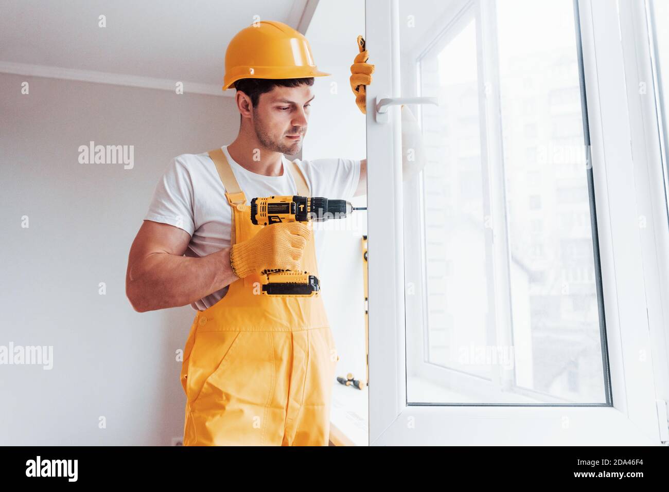 Handyman in yellow uniform installs new window by using automatic ...