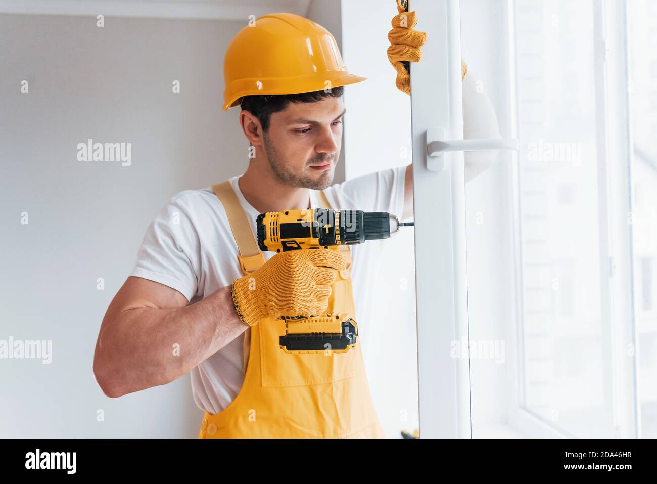 Handyman in yellow uniform installs new window by using automatic ...