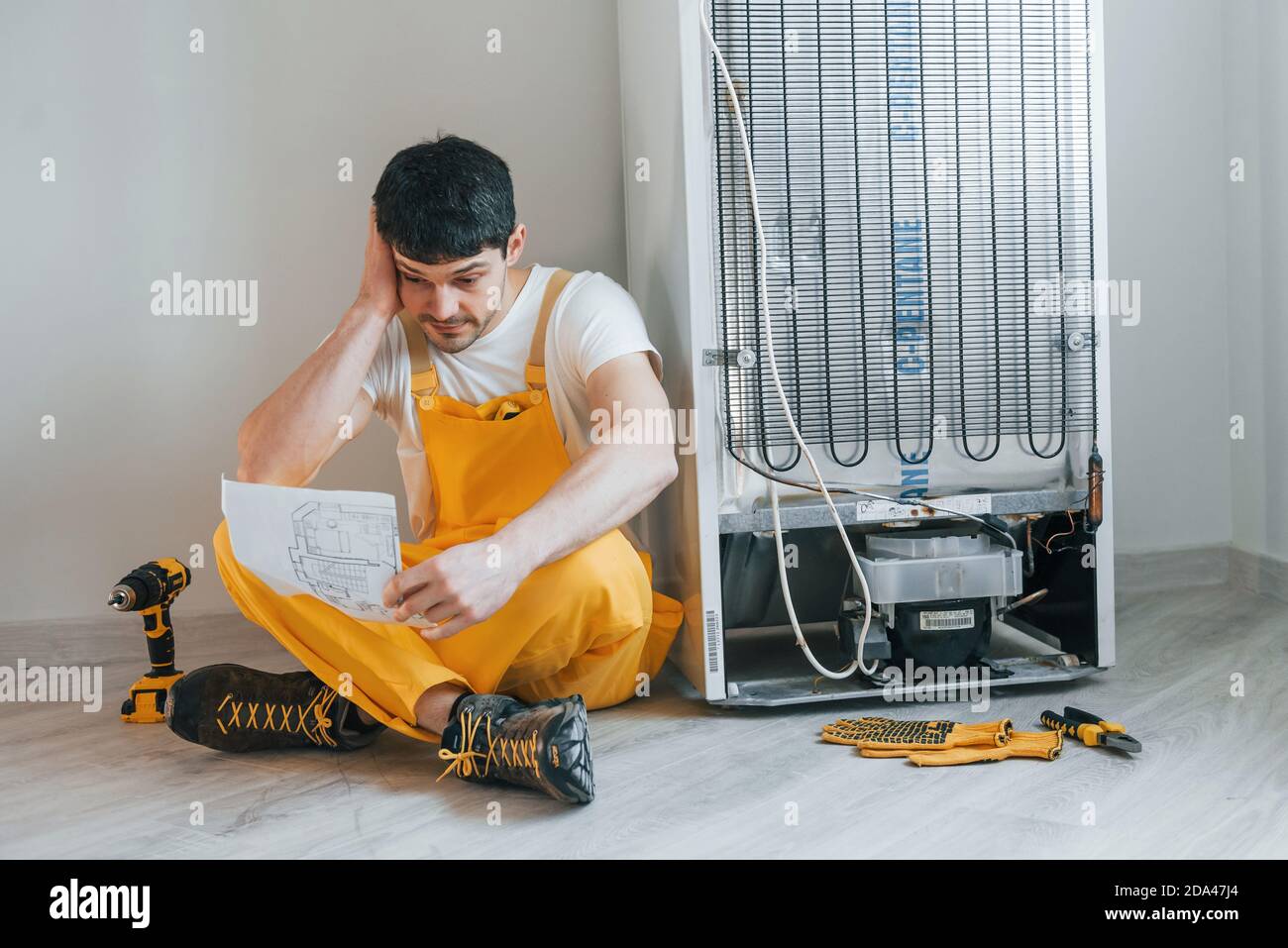 Confused handyman in yellow uniform reading manual for fridge indoors ...